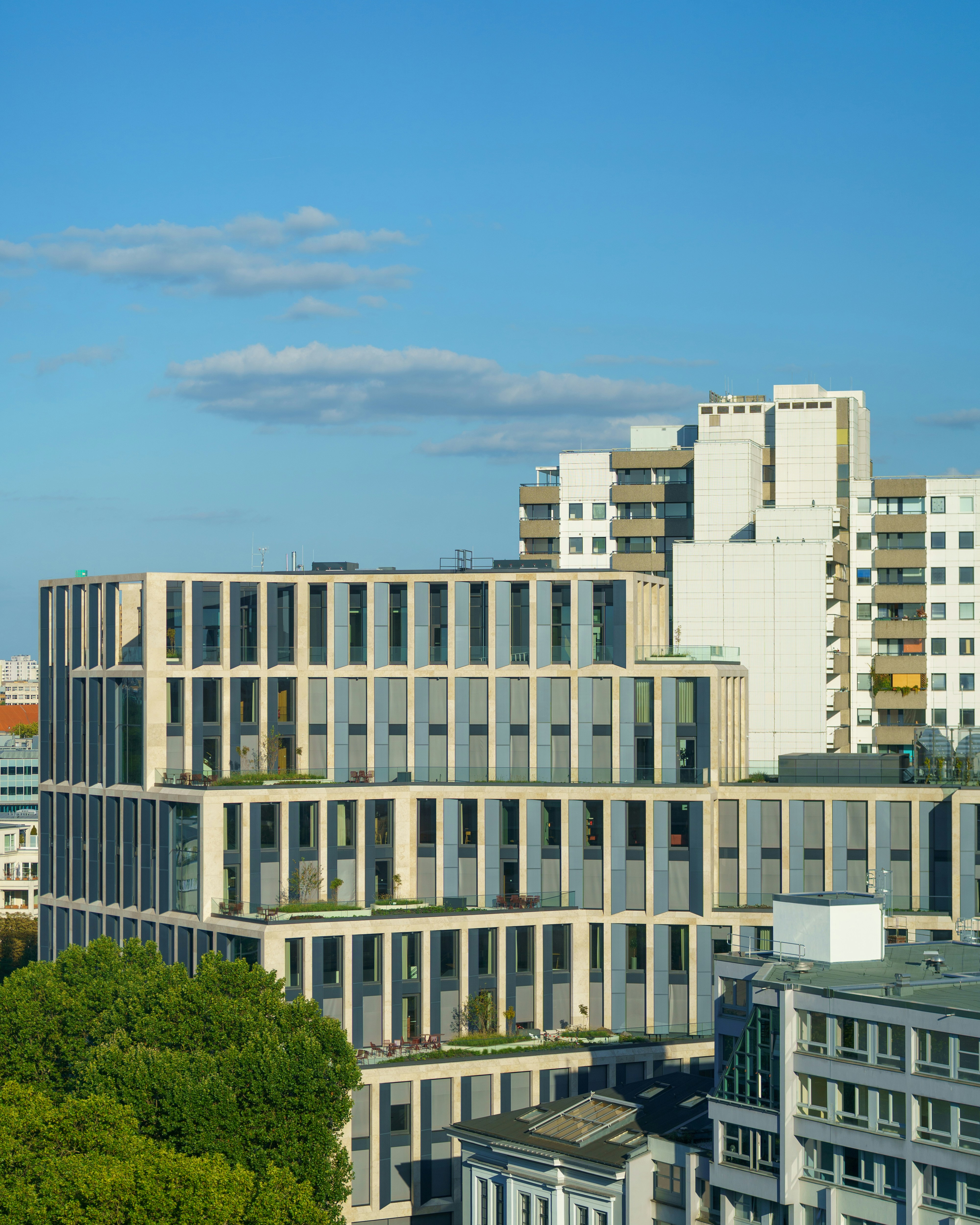 Contemporary buildings with distinctive geometric designs and lush greenery in the foreground. The scene showcases a blend of urban living and nature.