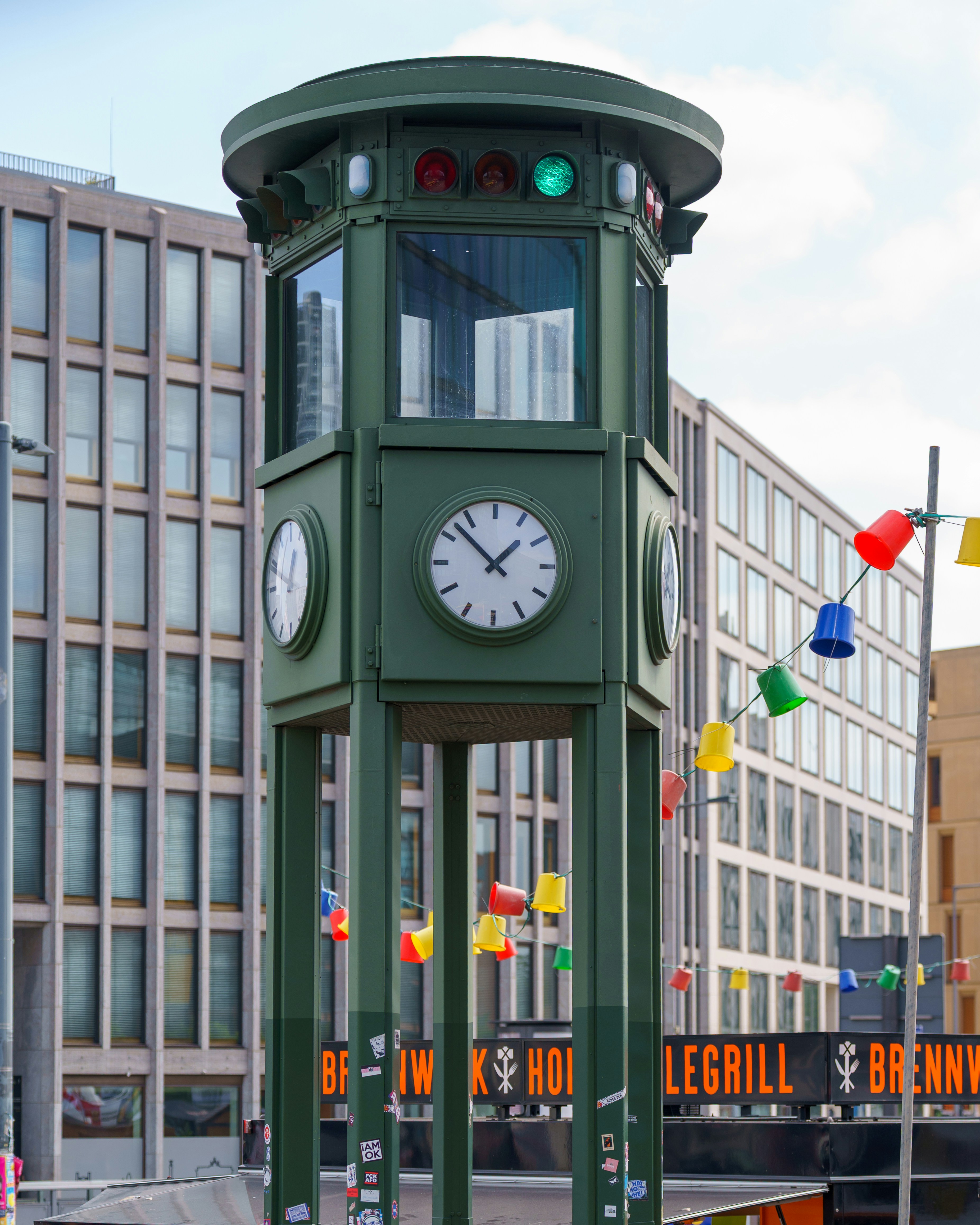 Green traffic light tower with clocks and colorful flags