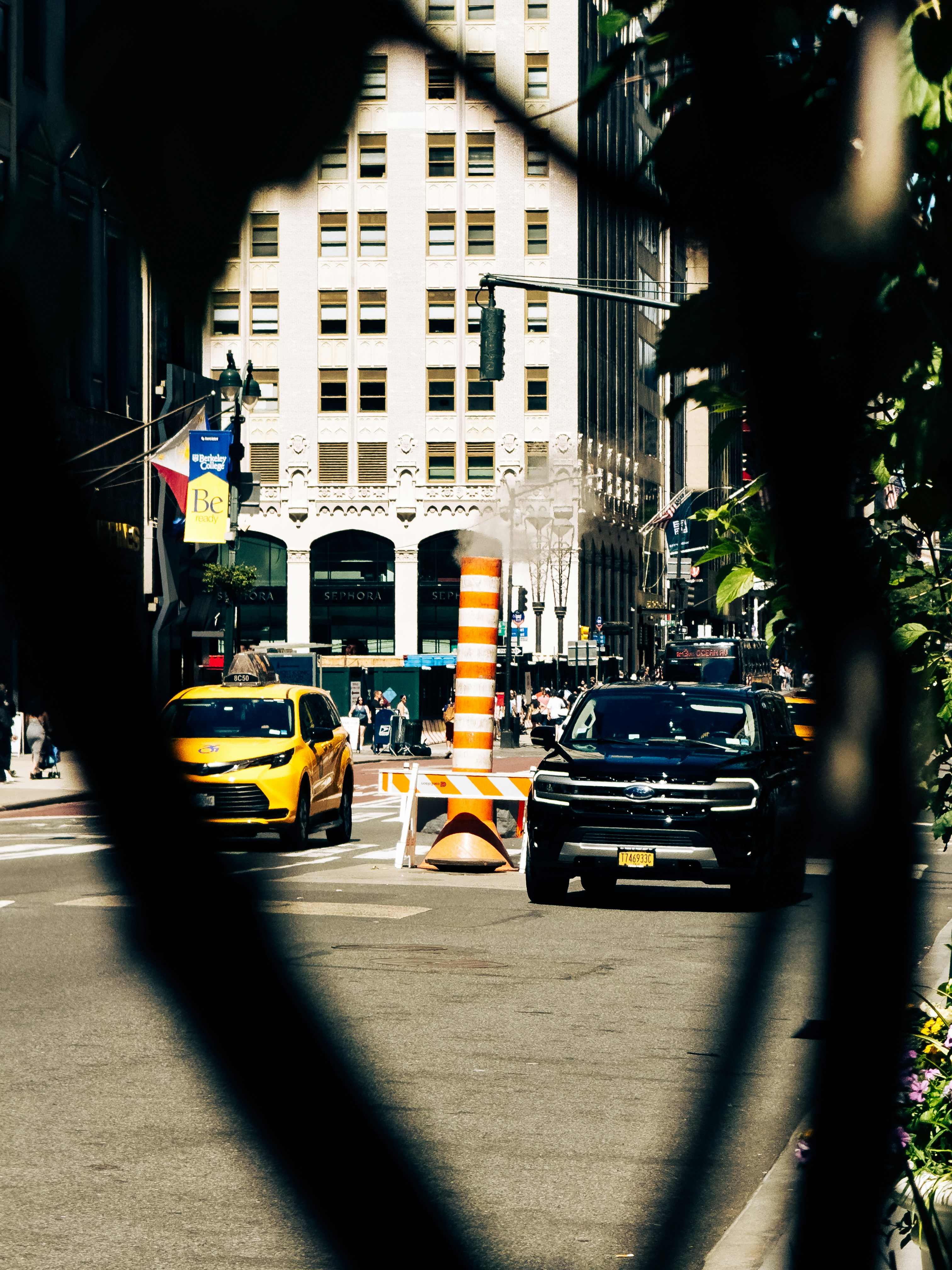 View of a bustling city street framed by foliage, showcasing traffic and architectural details in the background.