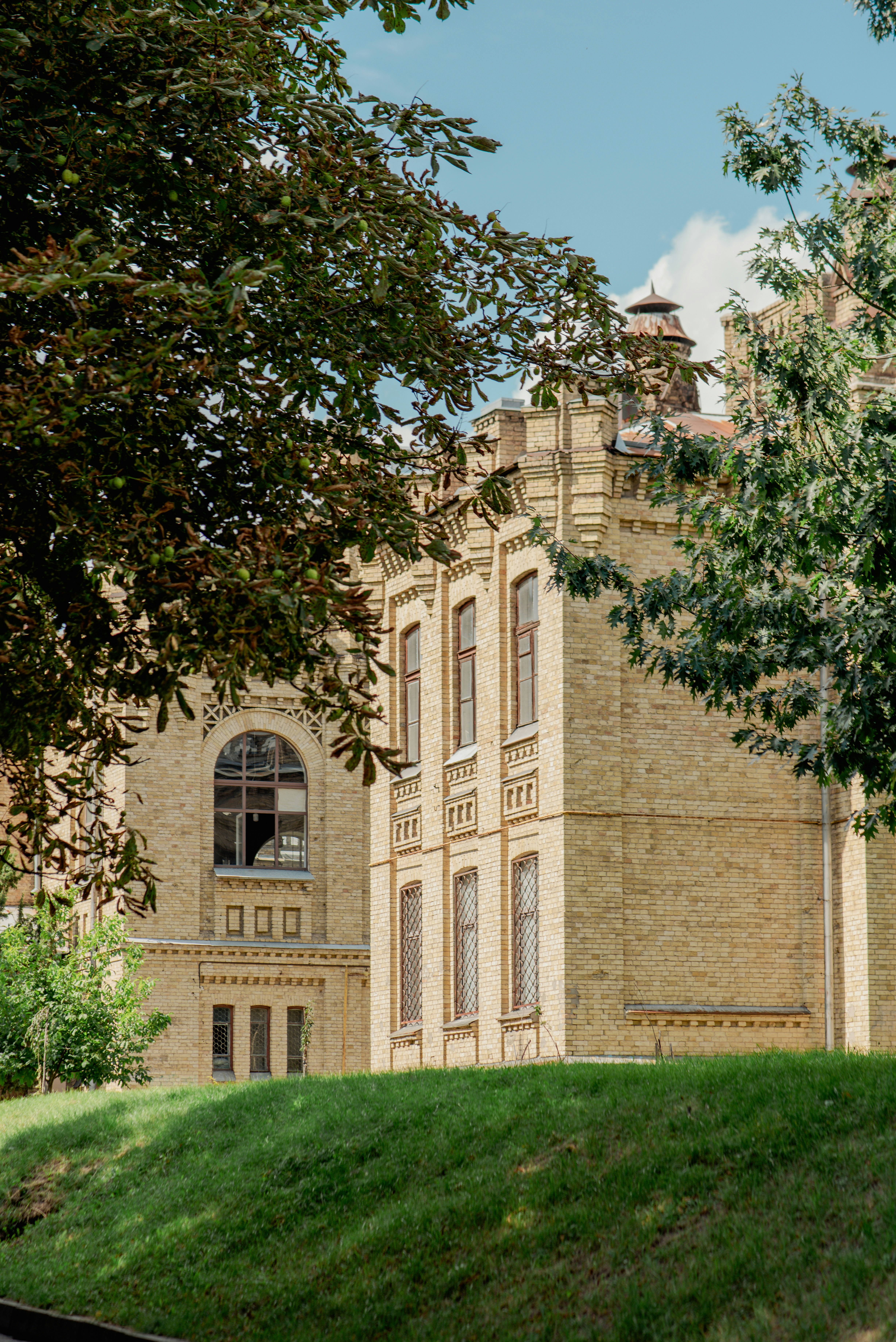 Old yellow brick building with arched window and trees.