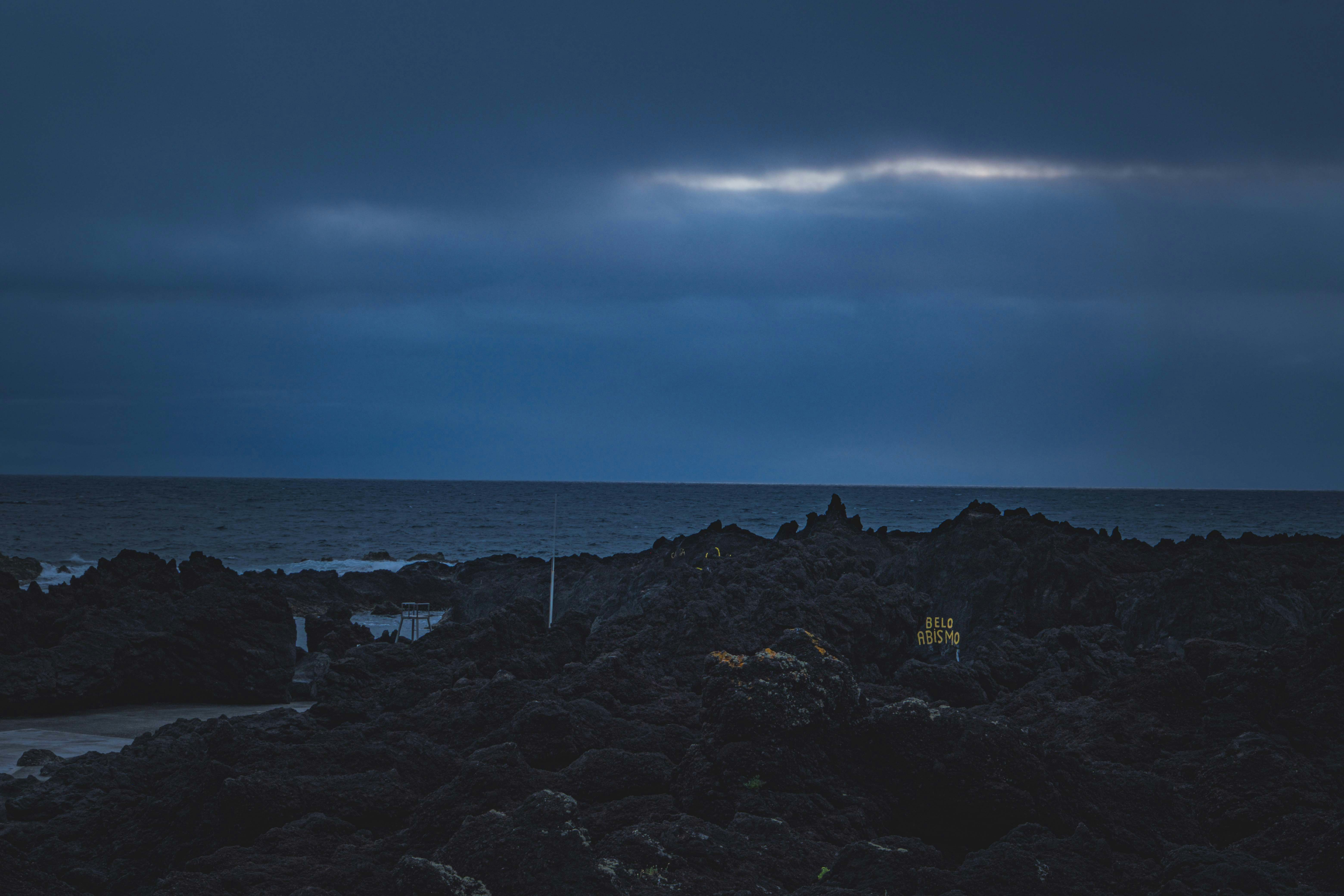 Rugged volcanic rocks meet the tranquil sea under a moody sky, hinting at the mysteries below the surface.