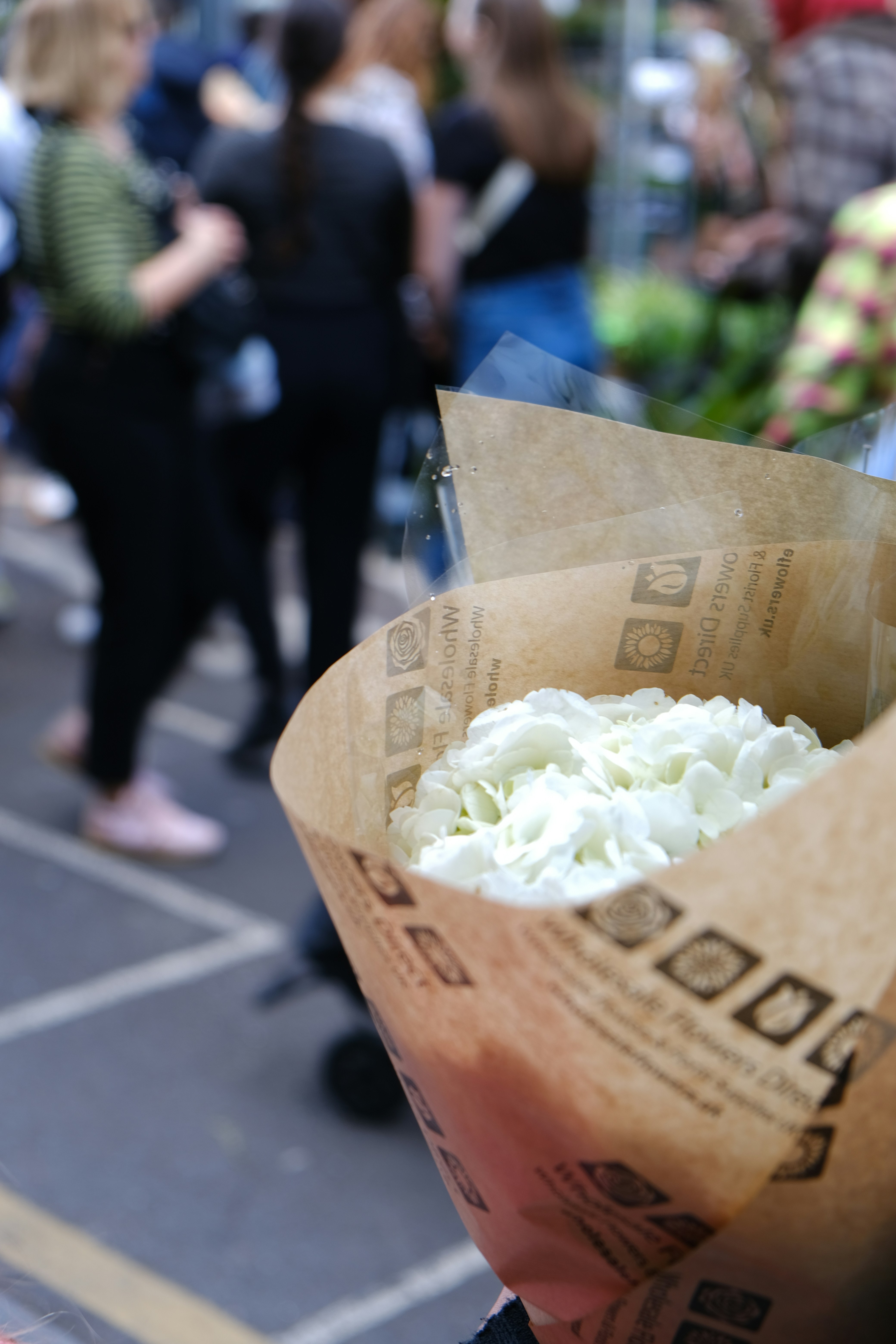 White Bouquet in Kraft Wrap, Quietly Framed by a City Crowd