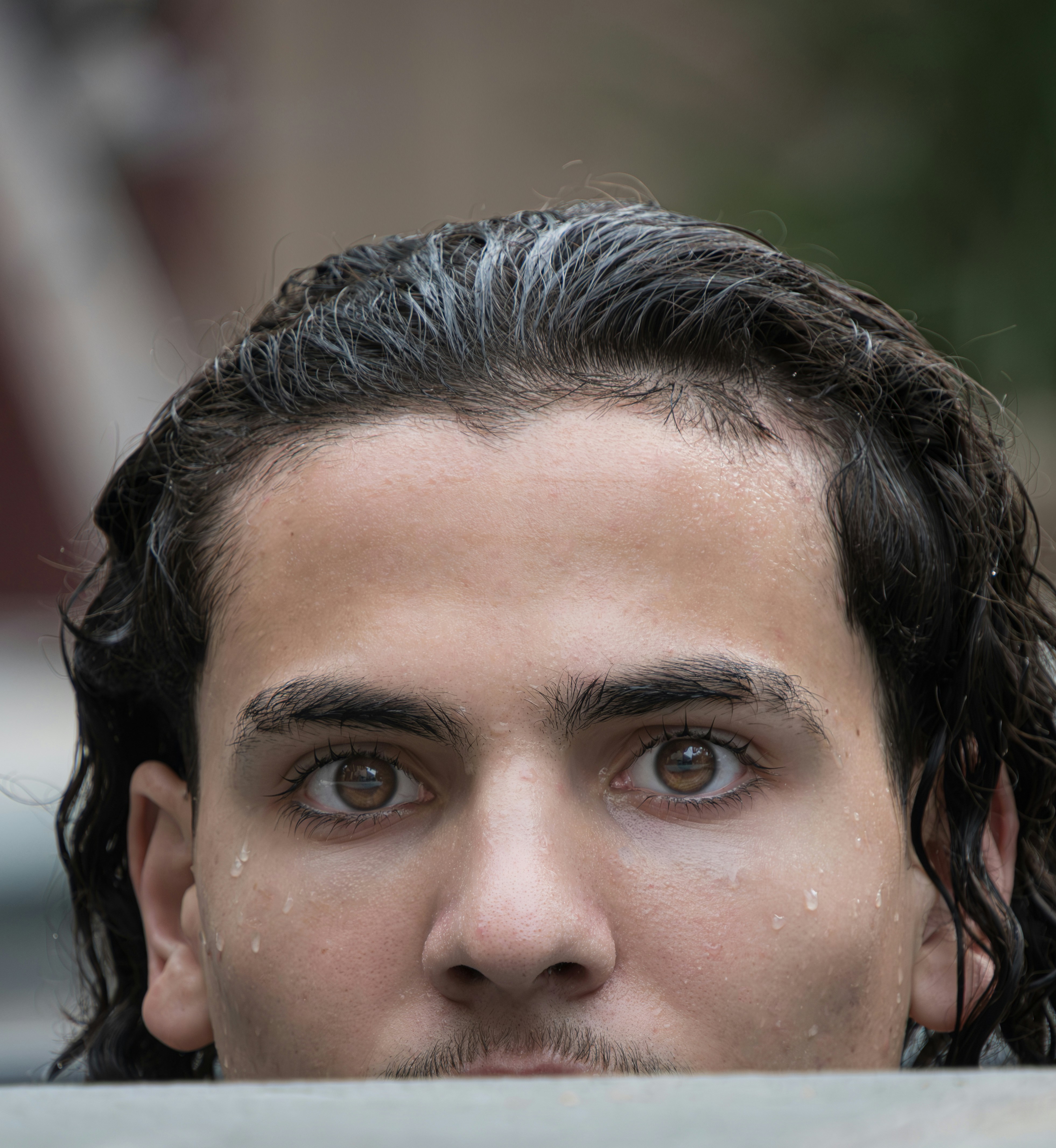 close up of teenager with wet hair peeking over ledge | Man with wet hair peeking over a ledge