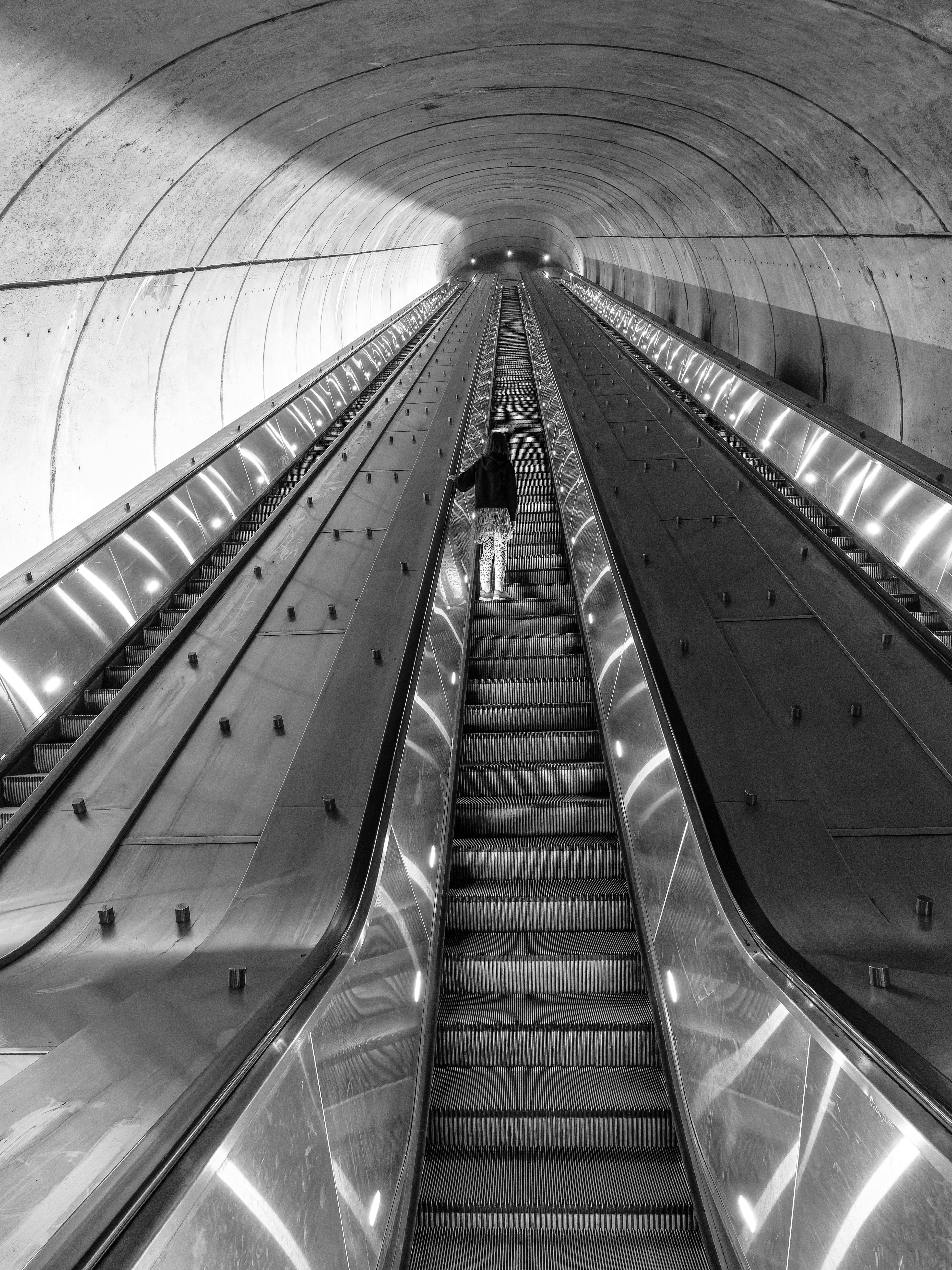 A very long escalator with a single person on it | Person ascends a long escalator in a subway station.