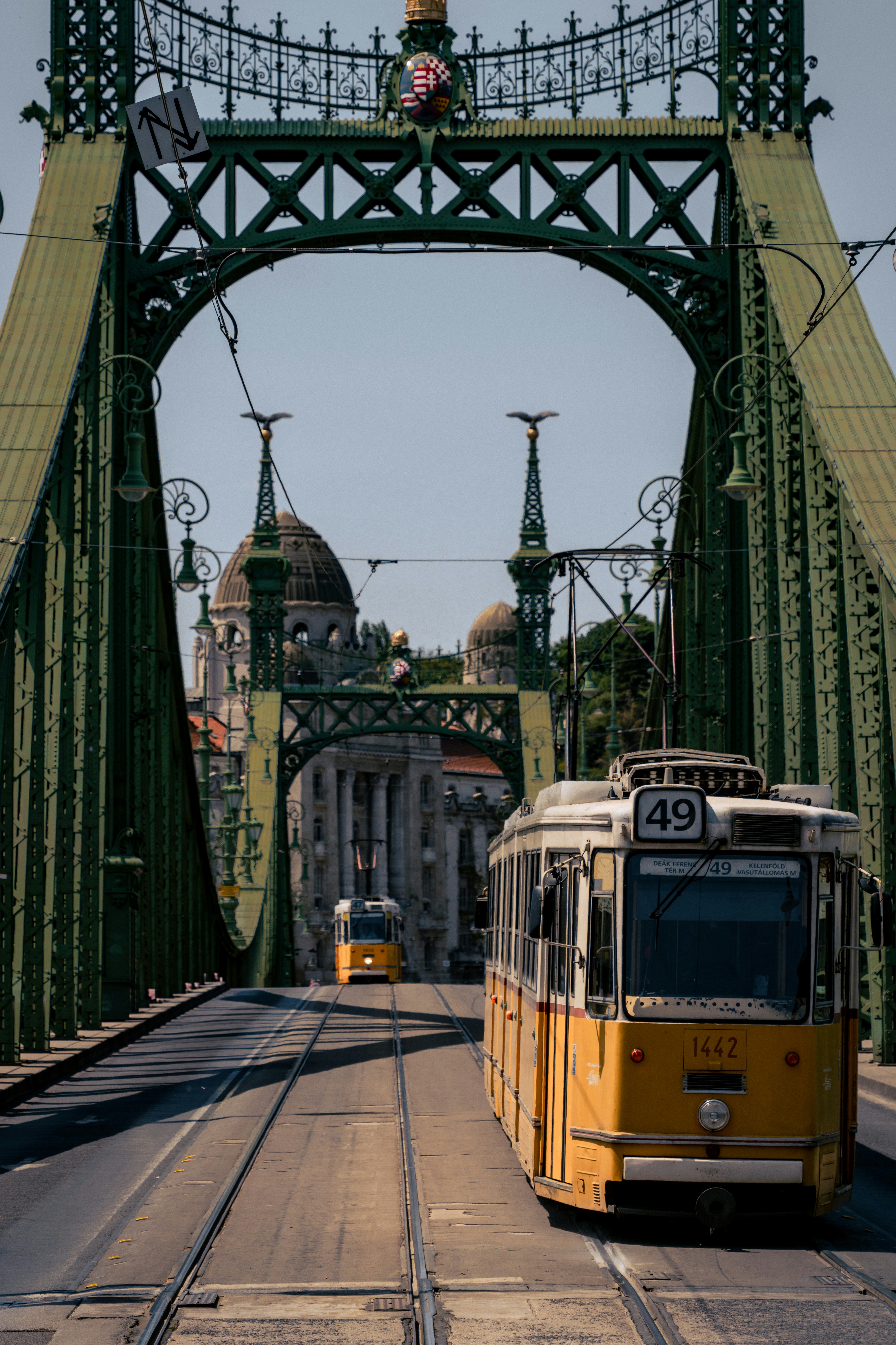 Yellow Tram Crossing the Green Iron Arch of a Historic Bridge