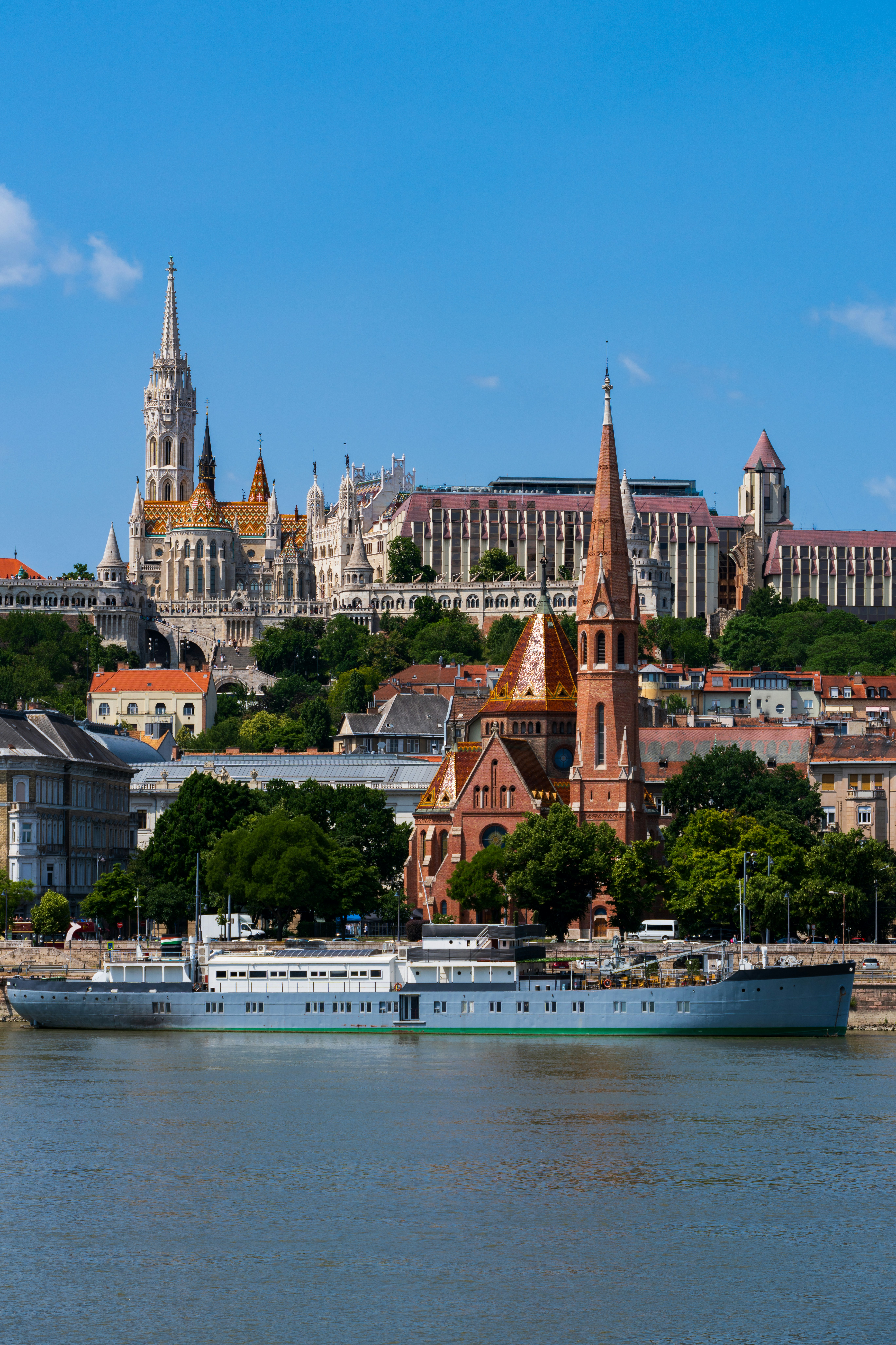 Viewing Buda from the Pest side of Danube. | Ship on river with historic buildings on hill