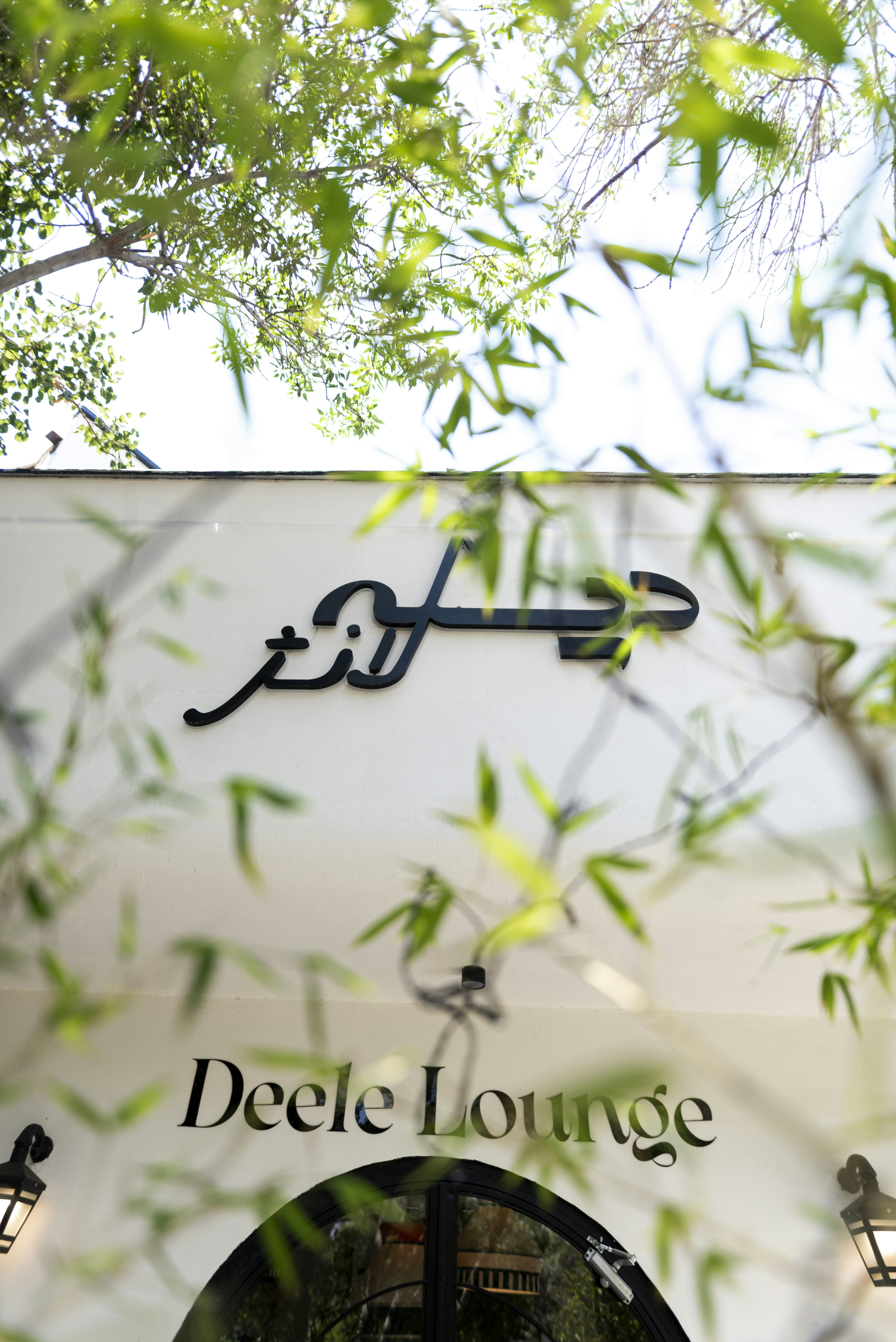 Stylish sign of Deele Lounge framed by lush greenery, highlighting a welcoming atmosphere.
