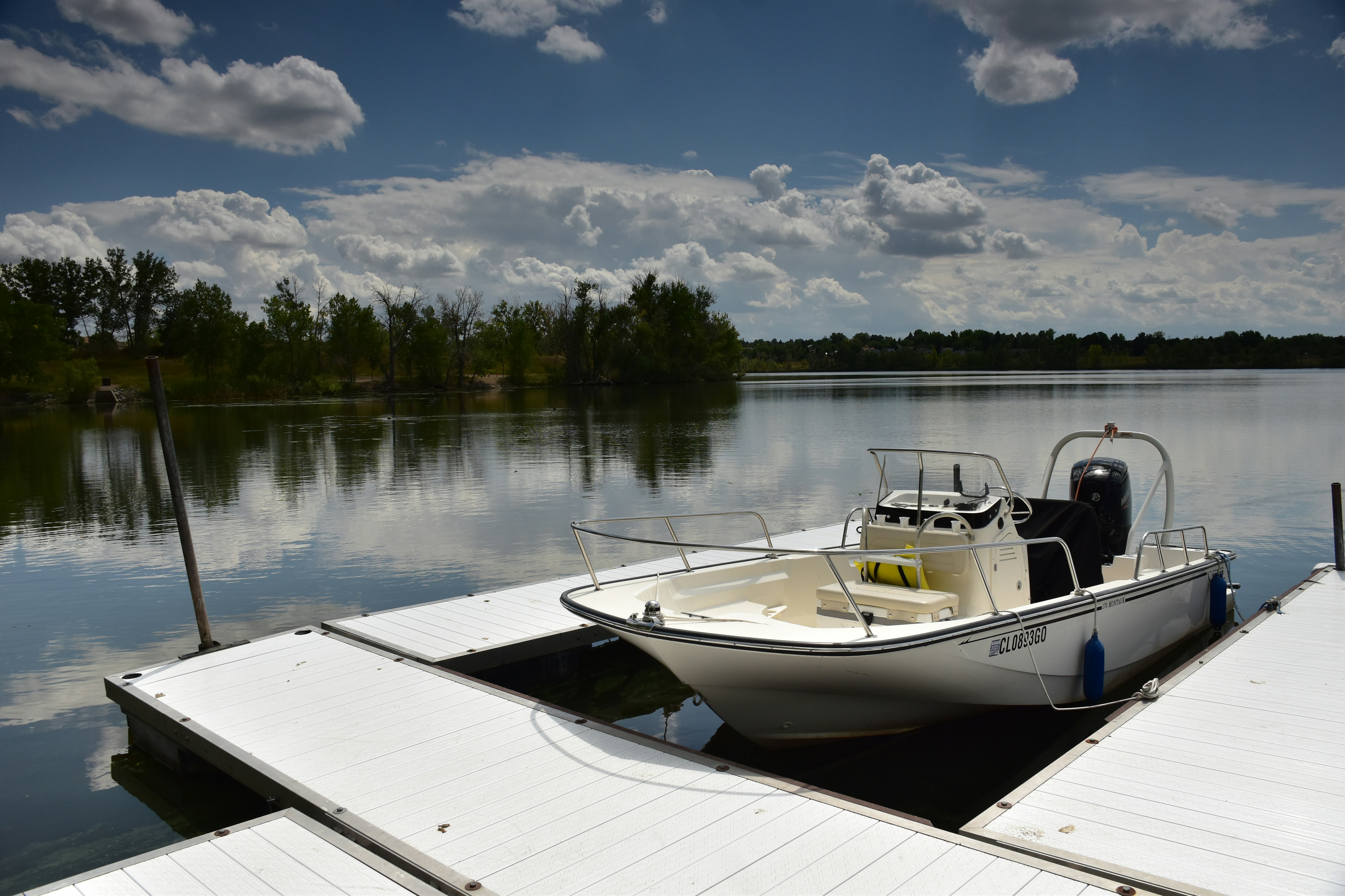 A boat resting peacefully at a dock, surrounded by calm waters and fluffy clouds reflecting the blue sky.