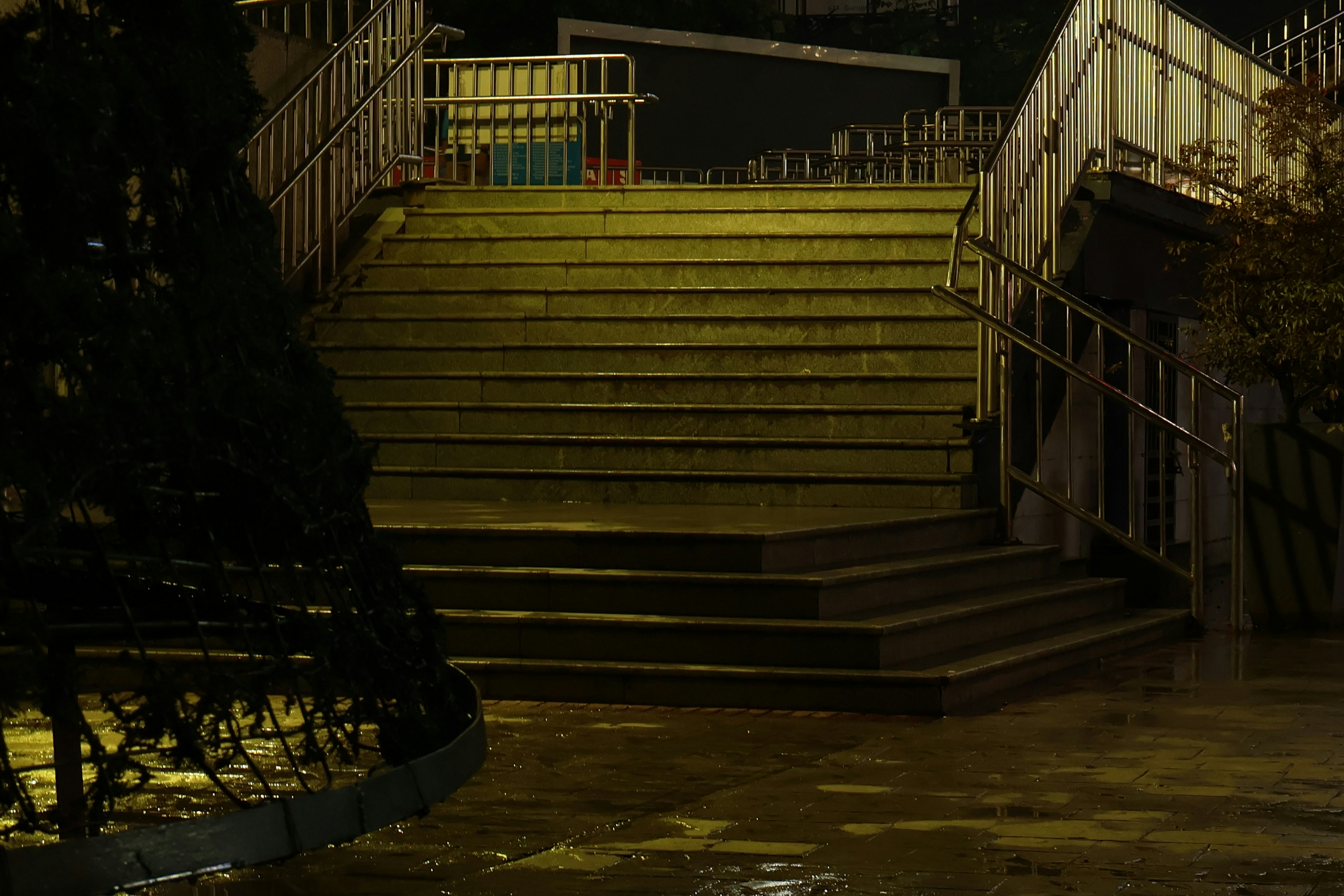 A zoomed in shot of an empty staircase at a metro station in Gurugam India. Yellow tones, city vibes, moody, still image | Wet outdoor stairs at night with yellow lighting