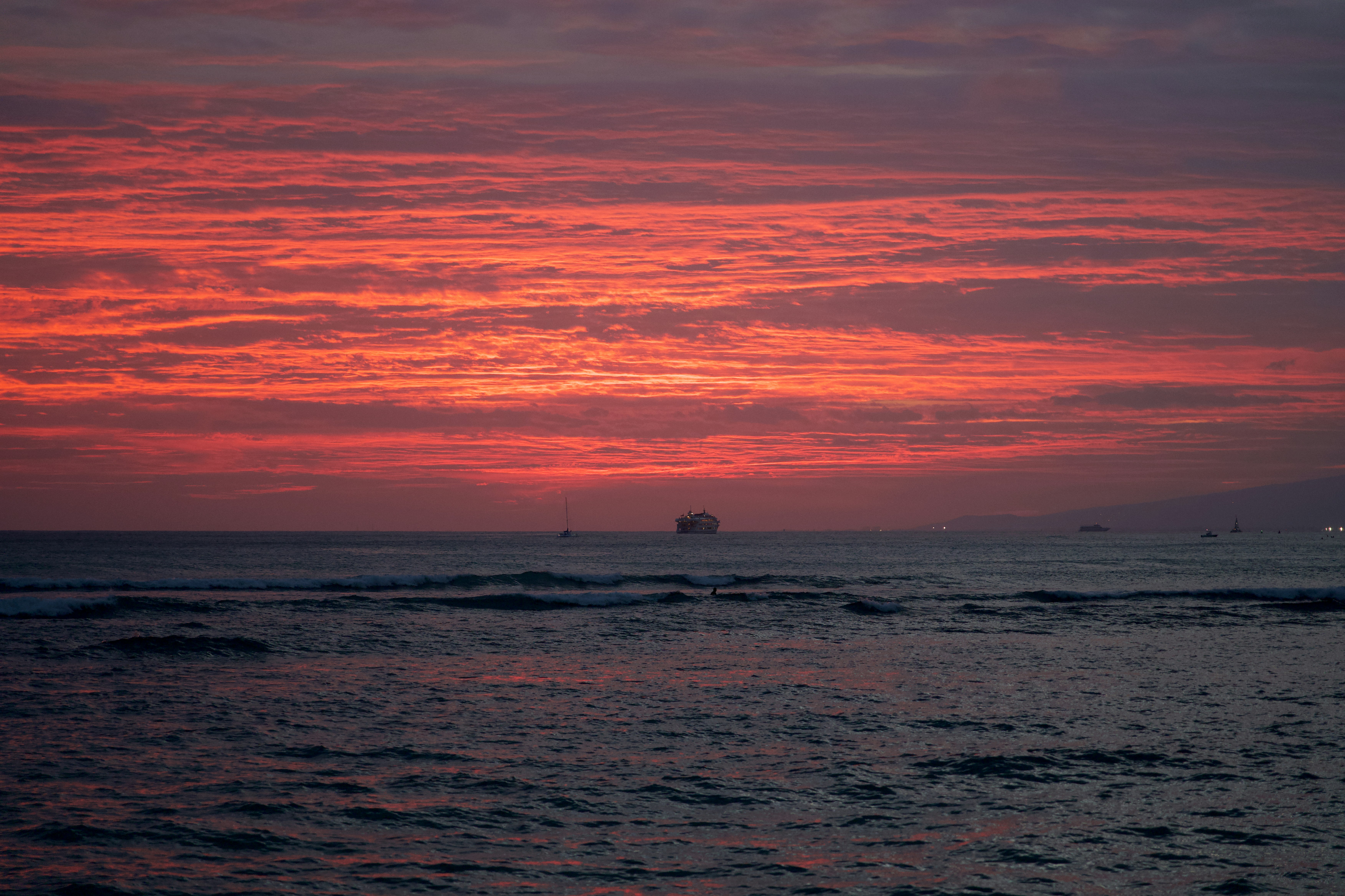 A breathtaking sunset over the ocean with fiery red and orange clouds painting the sky, reflecting softly on the calm waves | Vibrant red clouds over the ocean at sunset