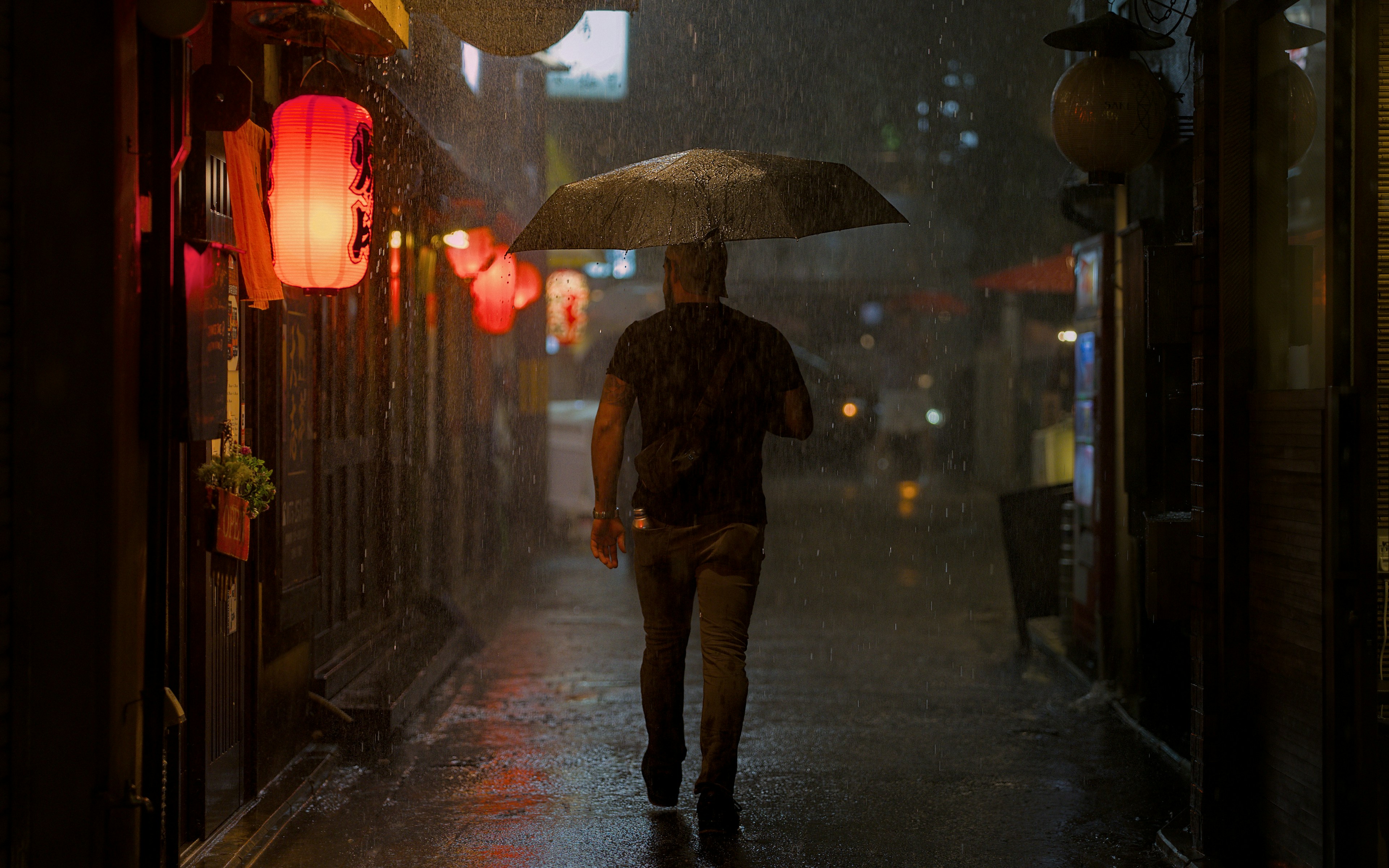 2025-06-10 | Man walks under umbrella on rainy city street at night
