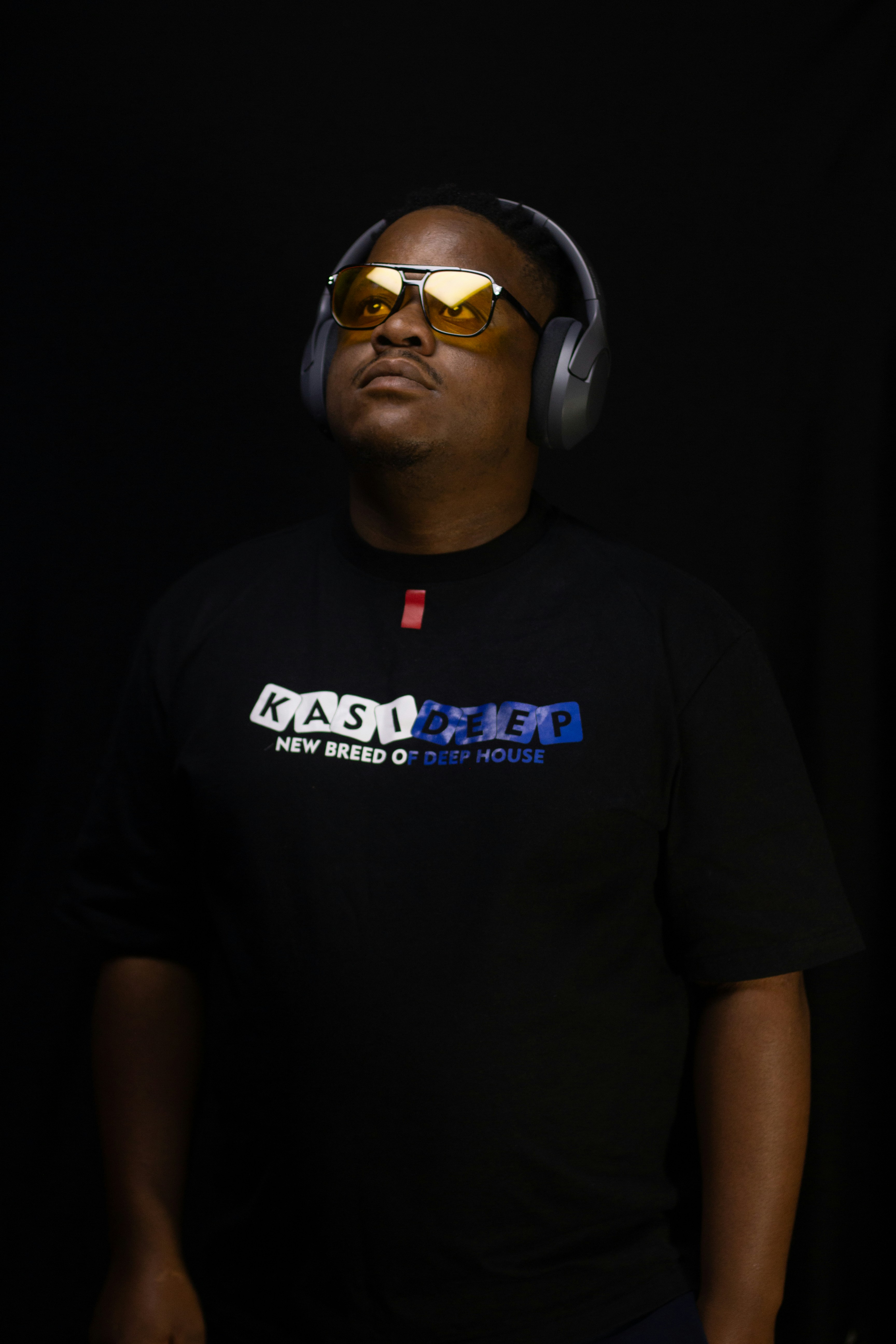A man wearing sunglasses and headphones stands confidently against a dark backdrop, embodying the spirit of deep house music culture.