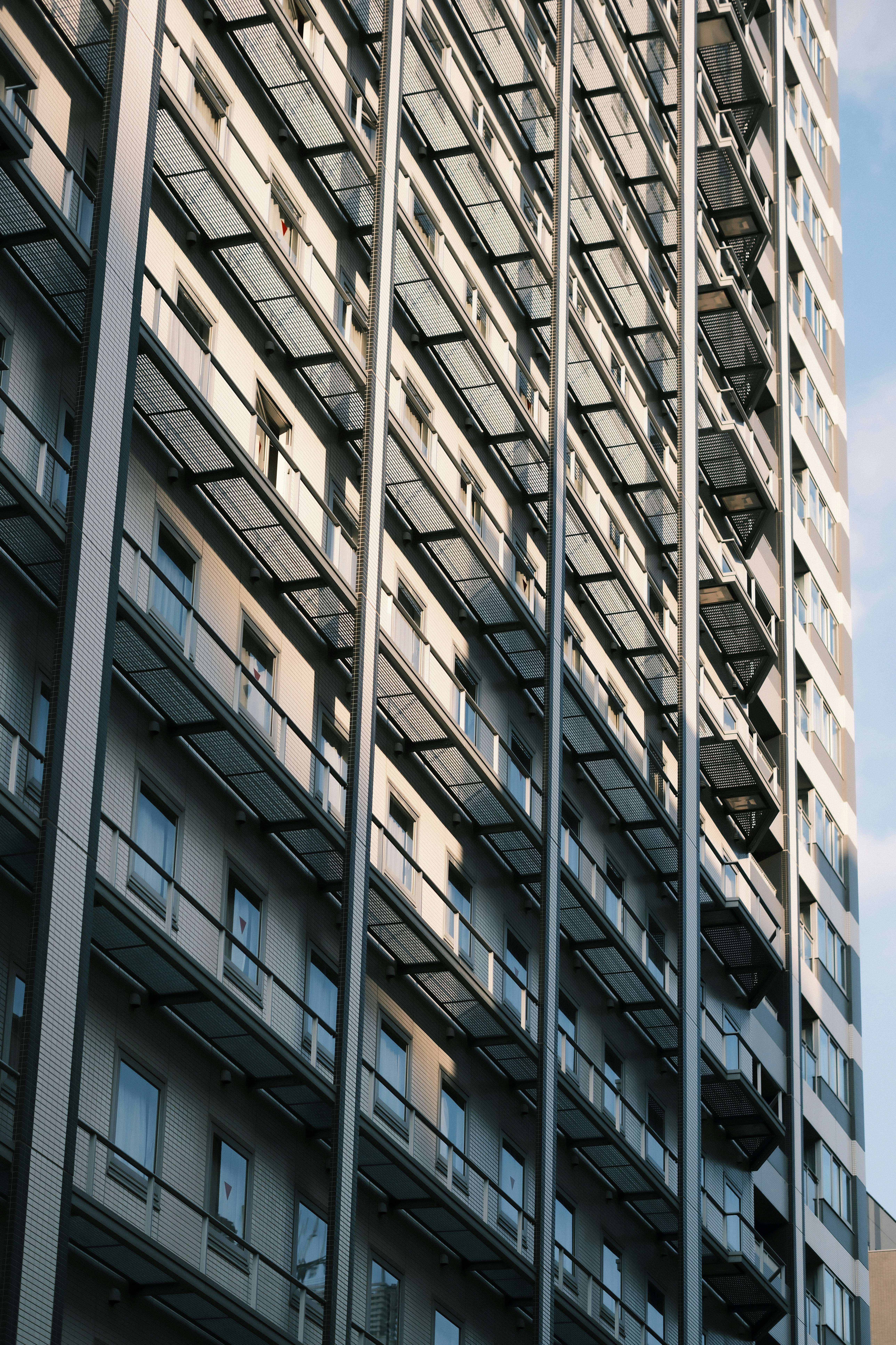 A modern residential building showcasing a grid of balconies and windows, bathed in warm afternoon light.