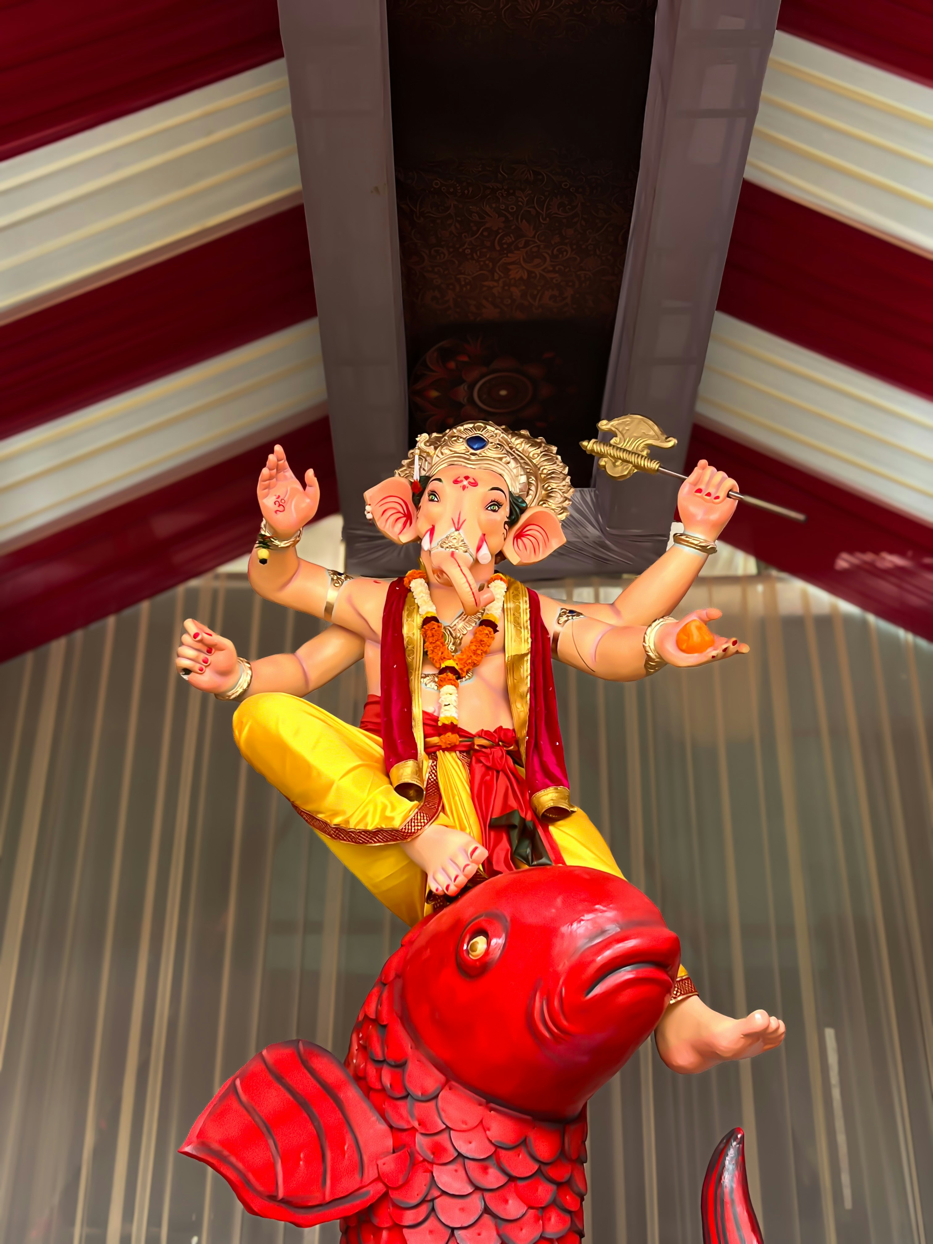 Giant Ganesh Statuette Emerging from a Red Fish Sculpture at a Decorated Shrine