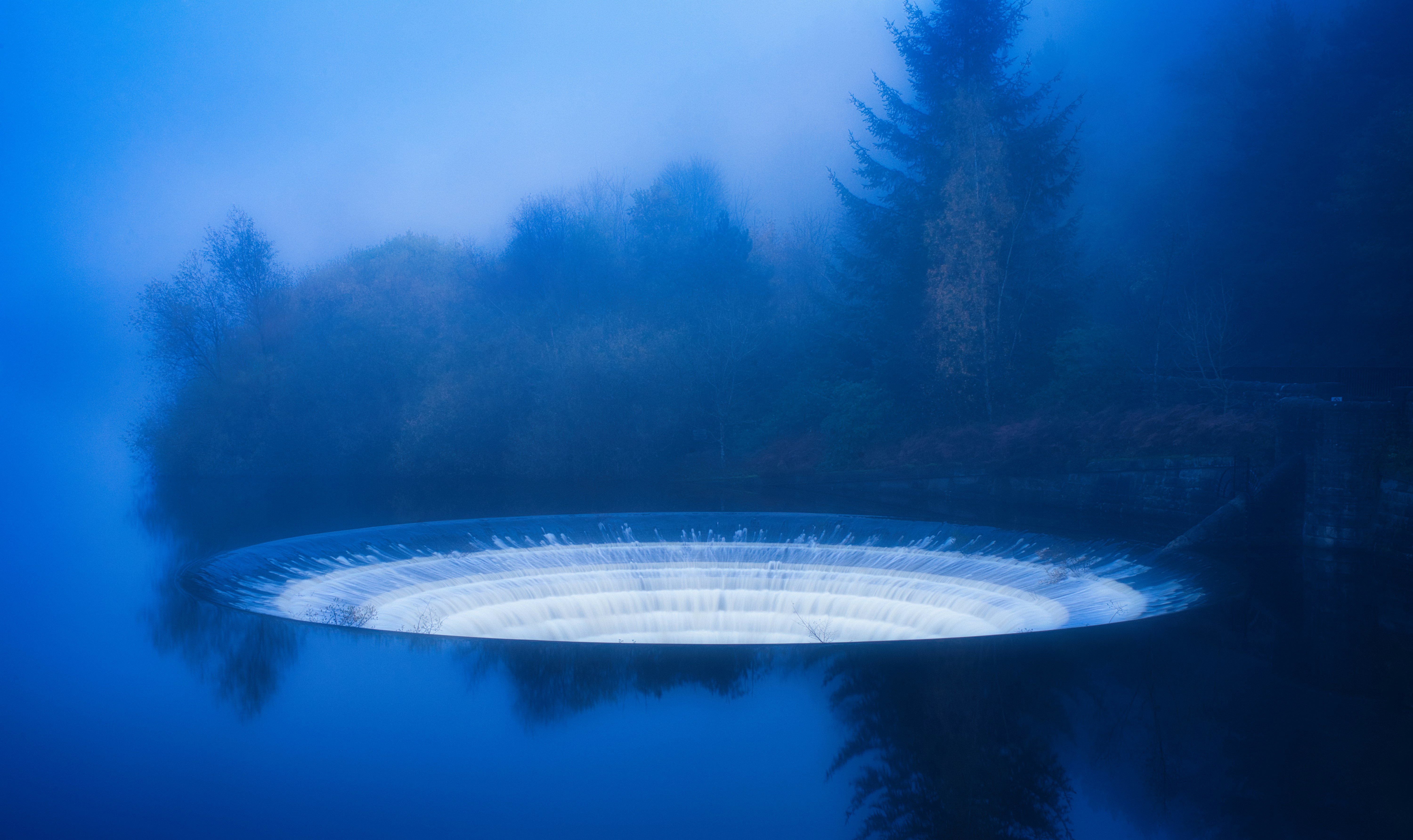 Ladybower Reservoir plughole on a foggy morning. | Glowing circular platform over misty blue water