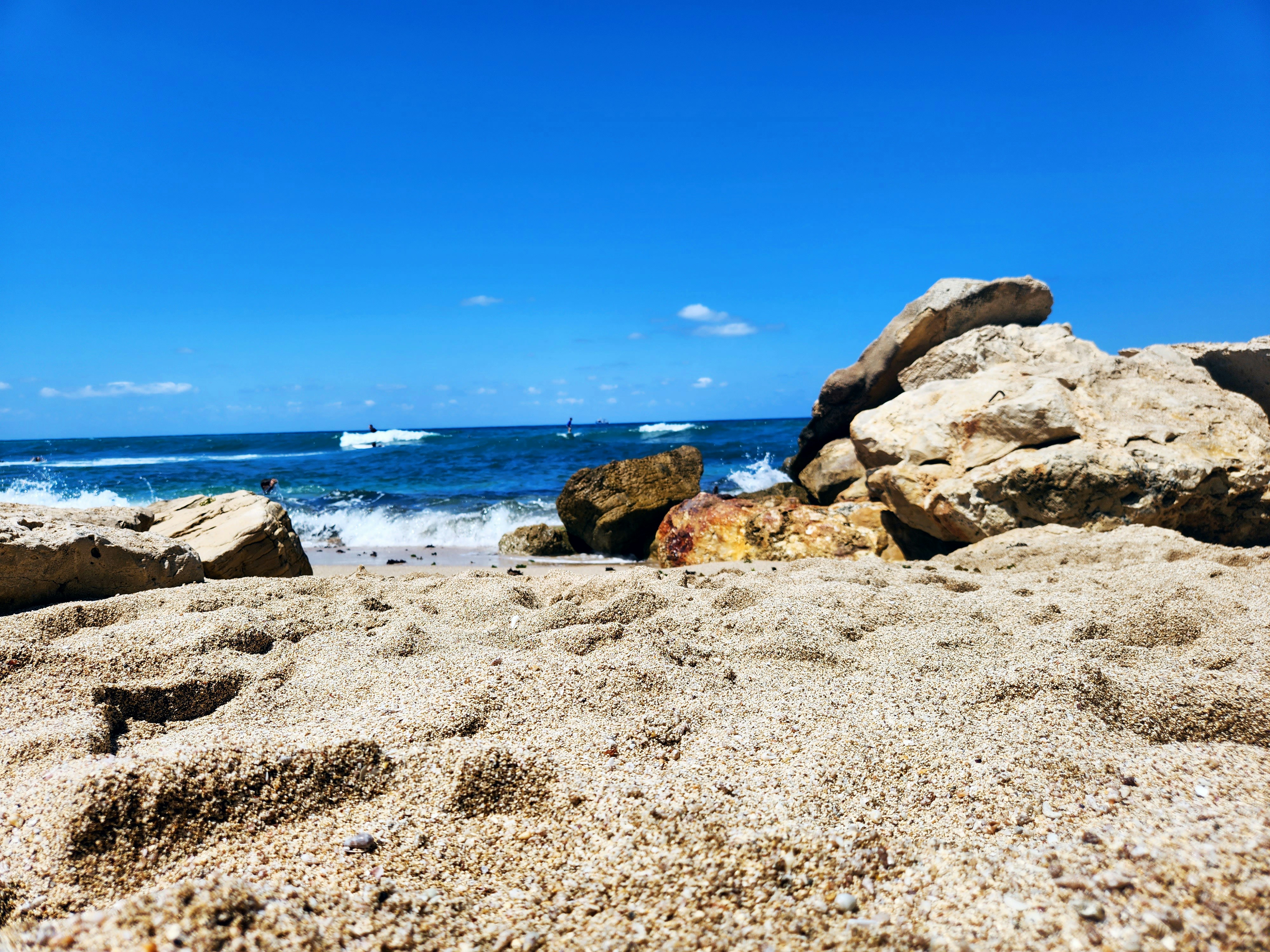 Beach Scene with Rocks Waves and Sandy Shore Under Blue Sky