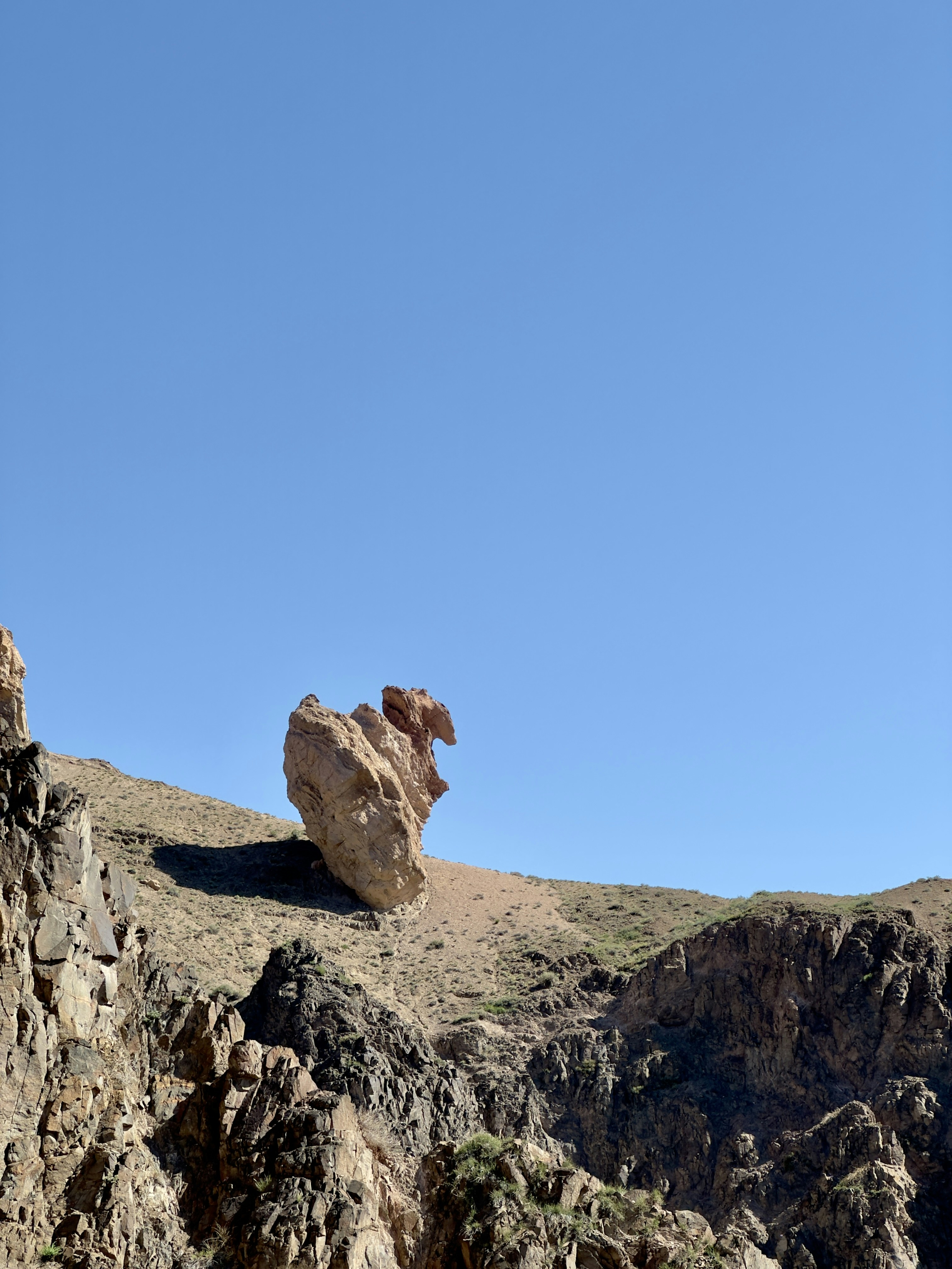 Large boulder balanced on a rocky hillside under blue sky