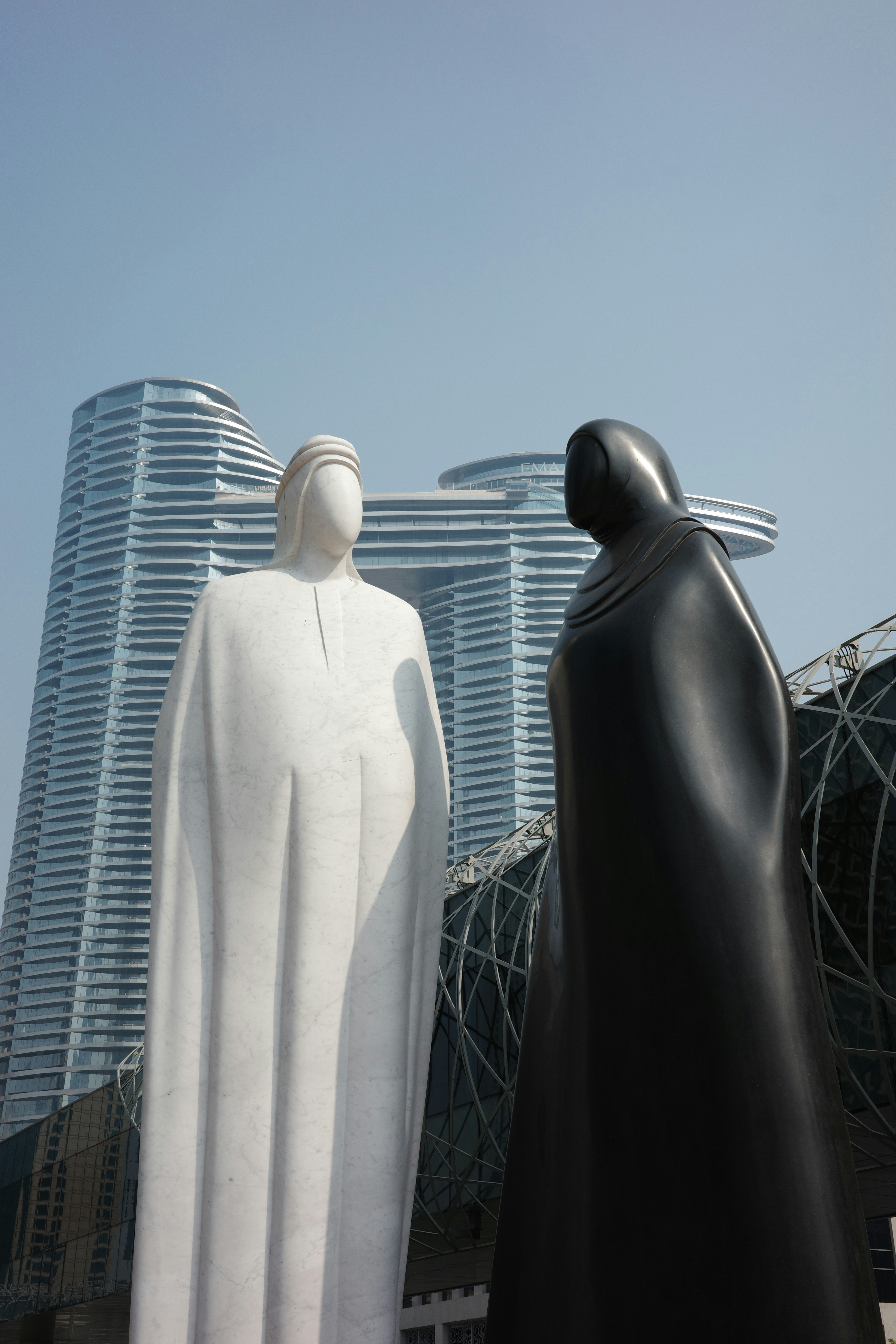 Two large sculptures, one white and one black, stand against a modern architectural backdrop, symbolizing contrast and duality.