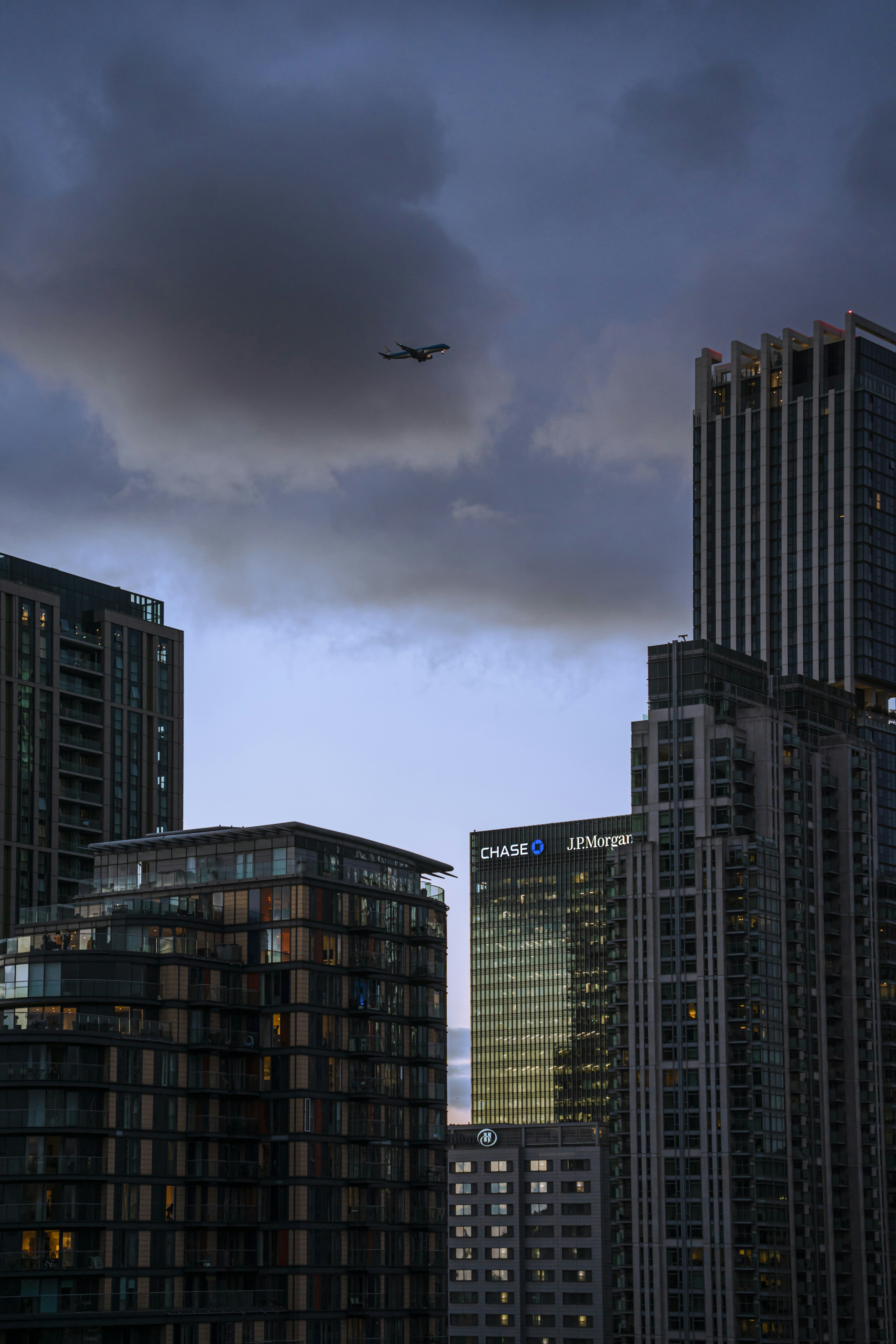Airplane flying over modern city buildings at dusk