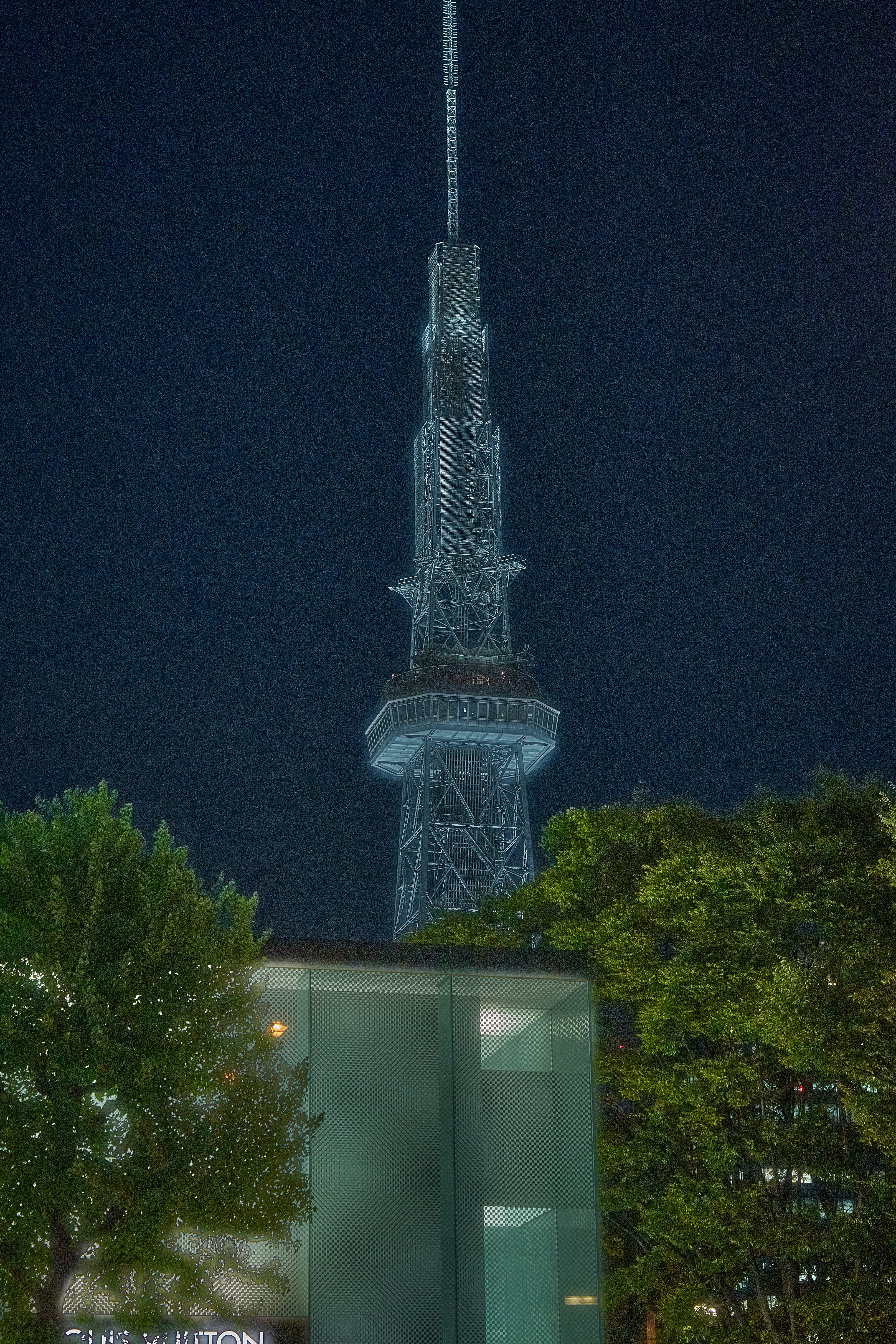 Tall radio tower illuminated at night with trees