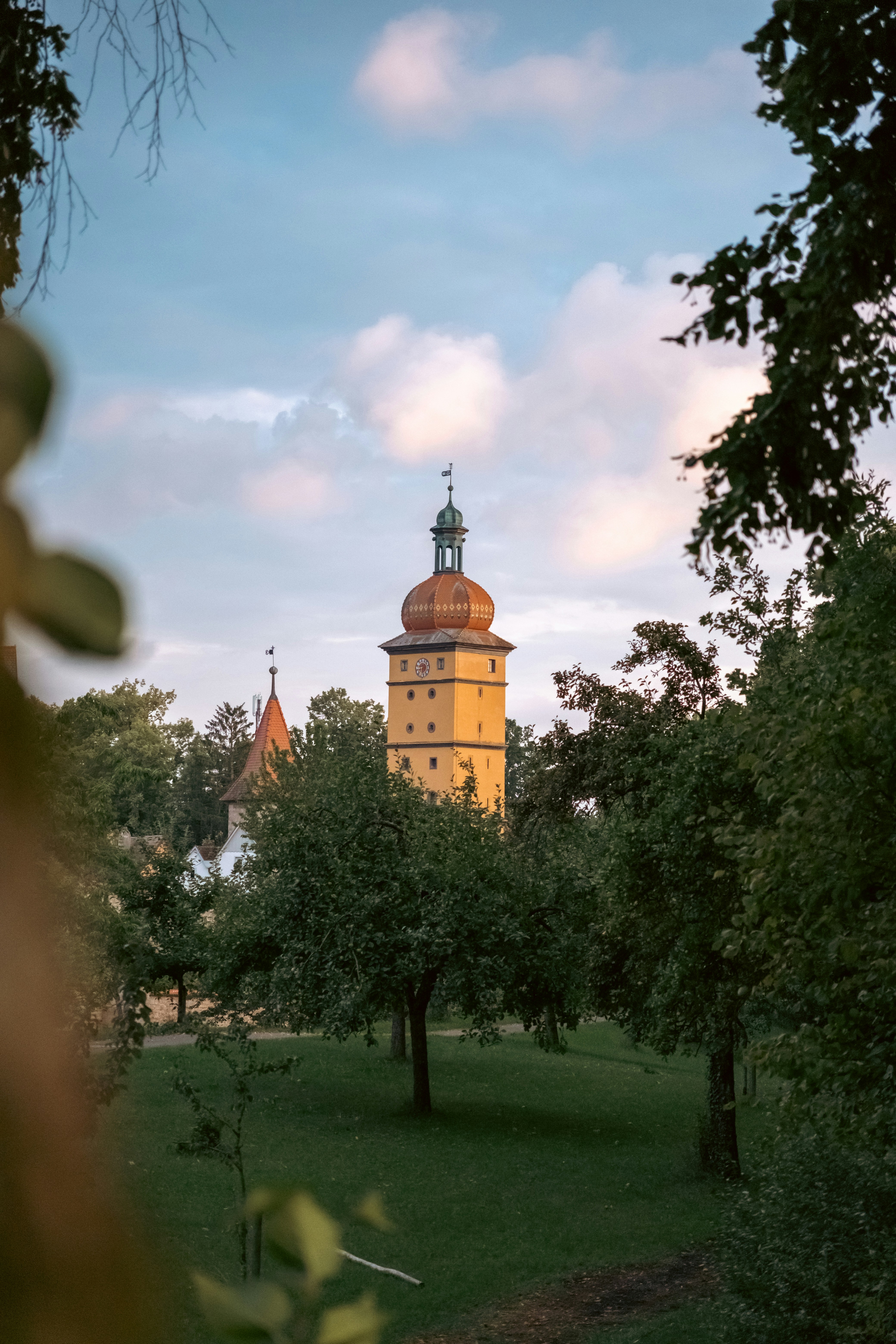 Historic tower rising above lush greenery under a pastel sky, showcasing architectural charm and natural beauty.