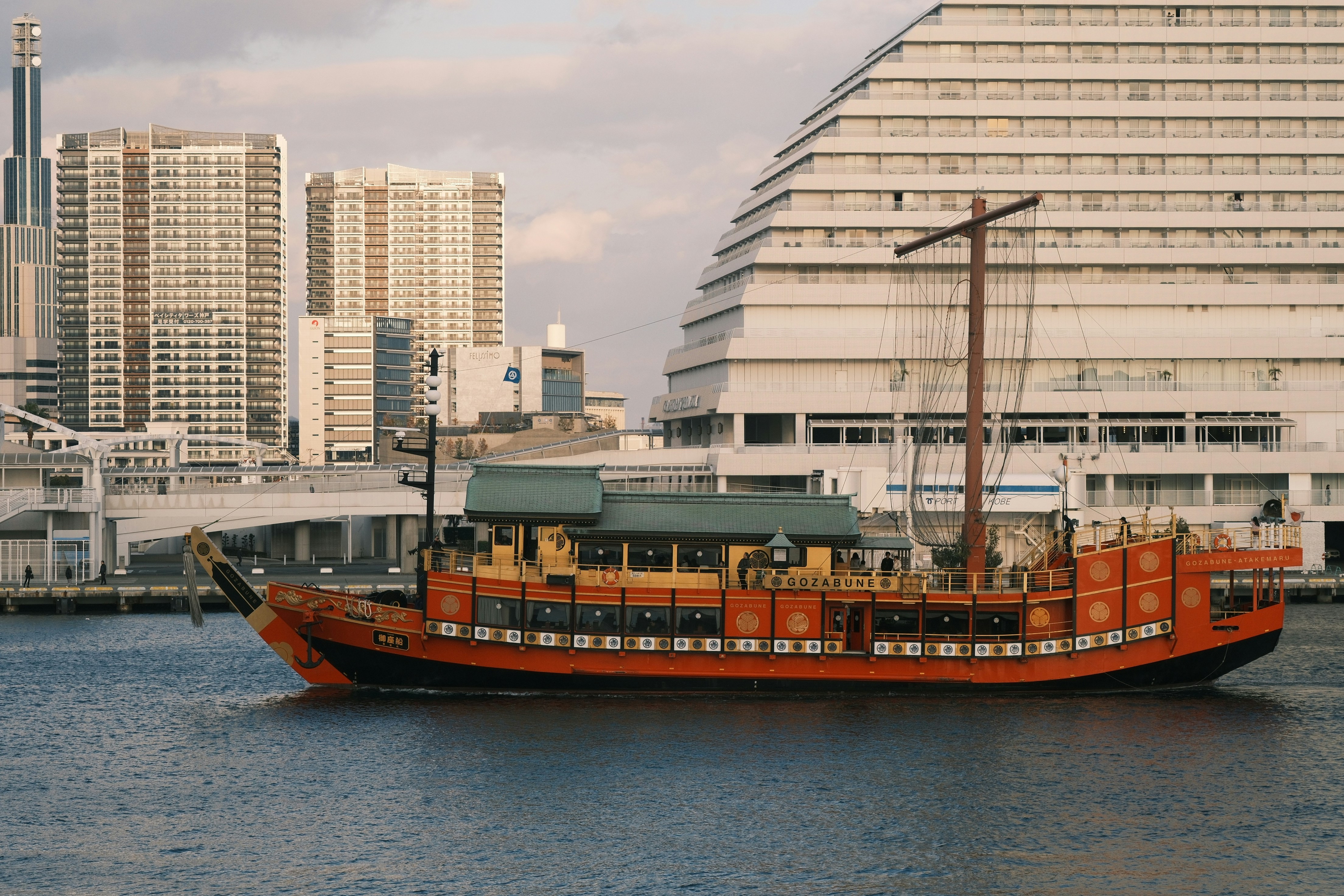 Traditional japanese boat sails in a modern harbor.
