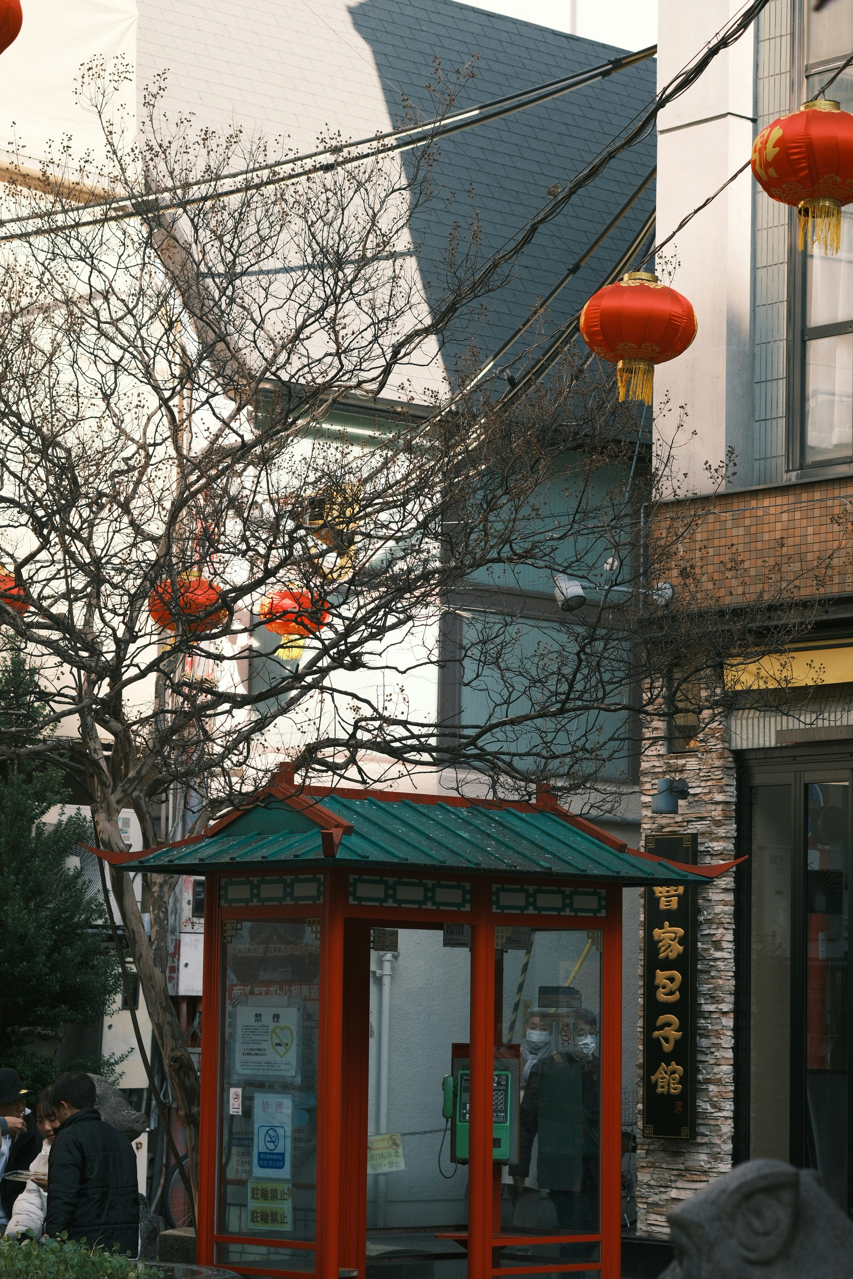 Red chinese lanterns hang near a traditional phone booth.