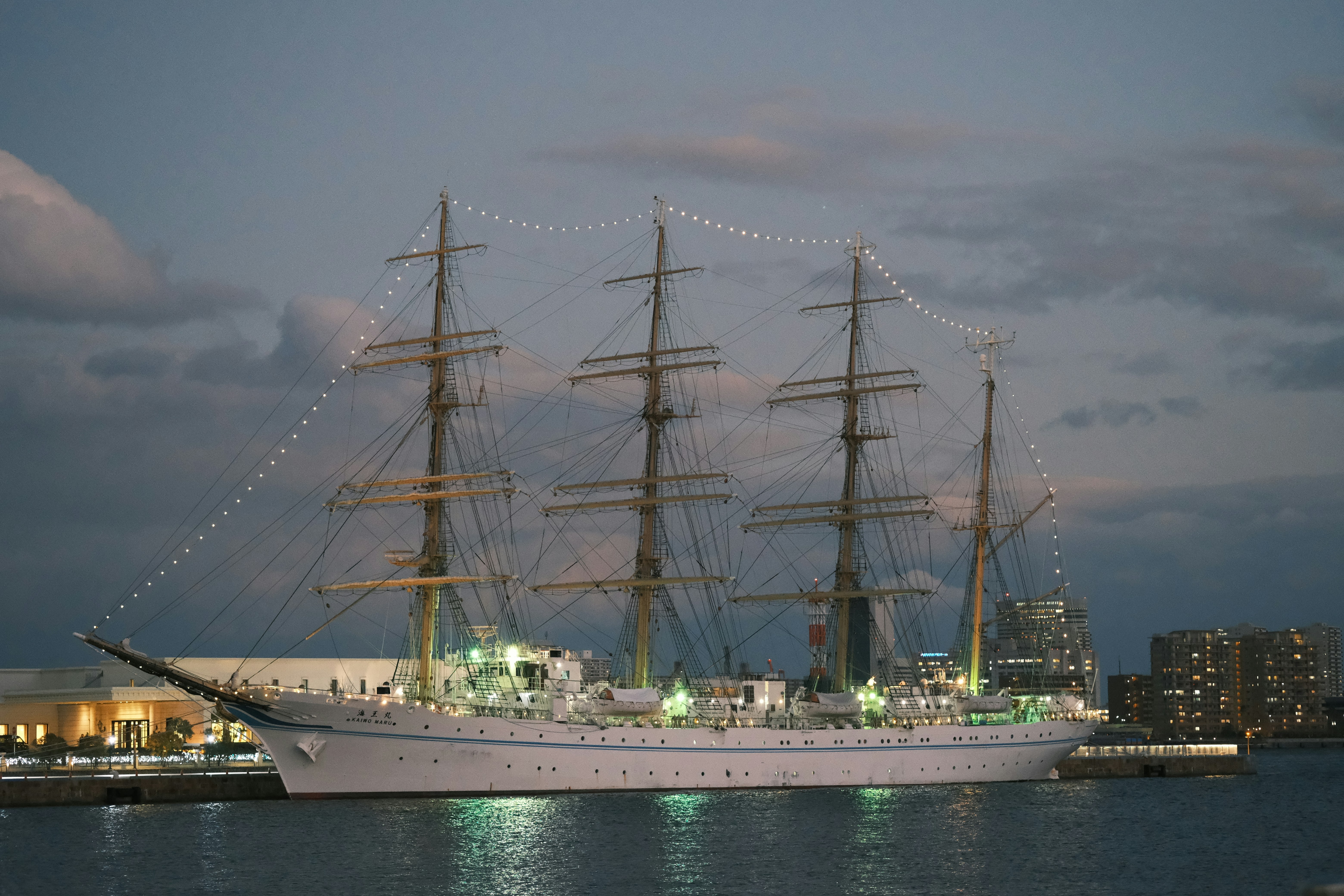 Tall ship illuminated at dusk with city lights in background