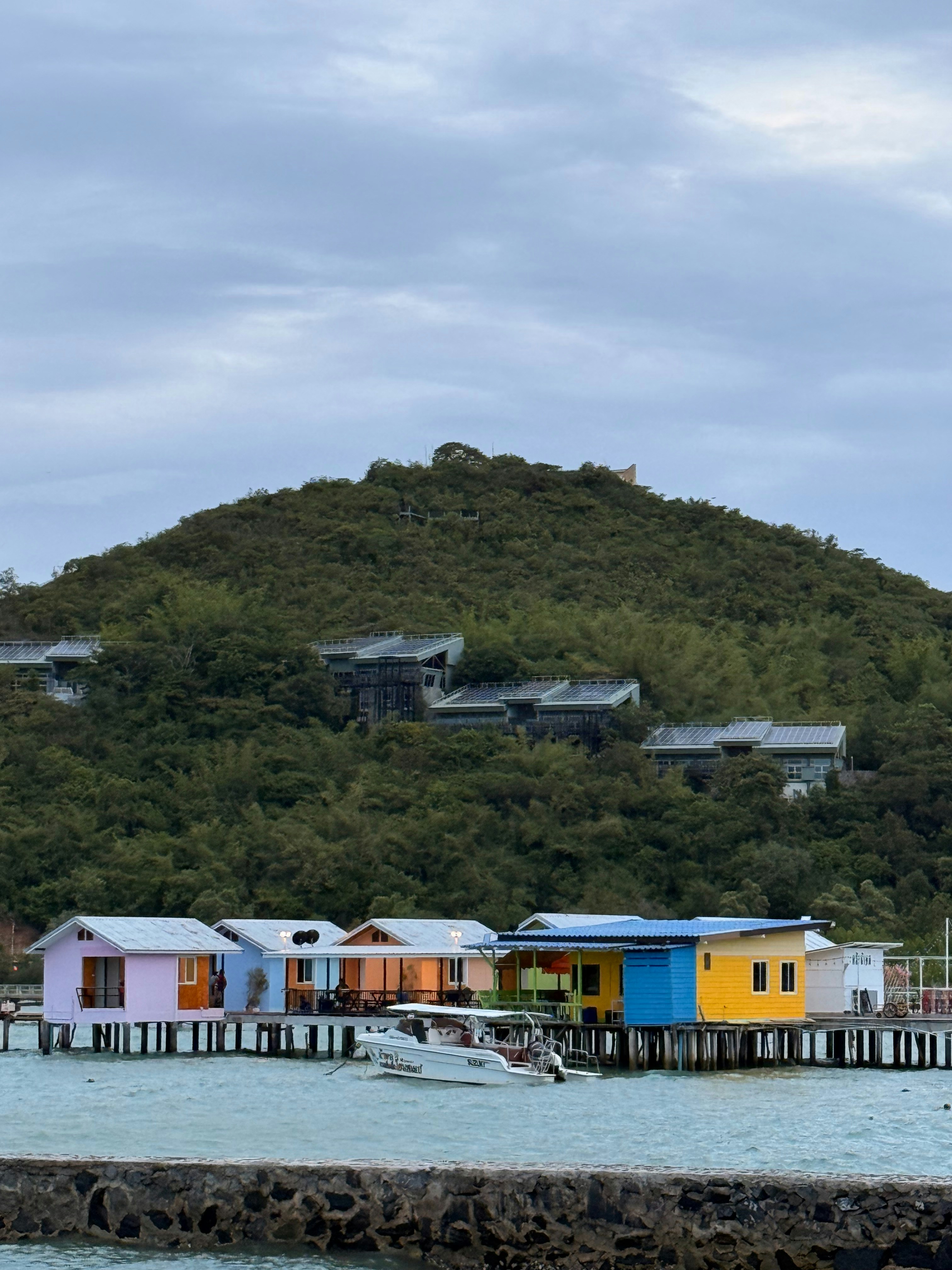 Colorful stilt houses on the water with a hill.