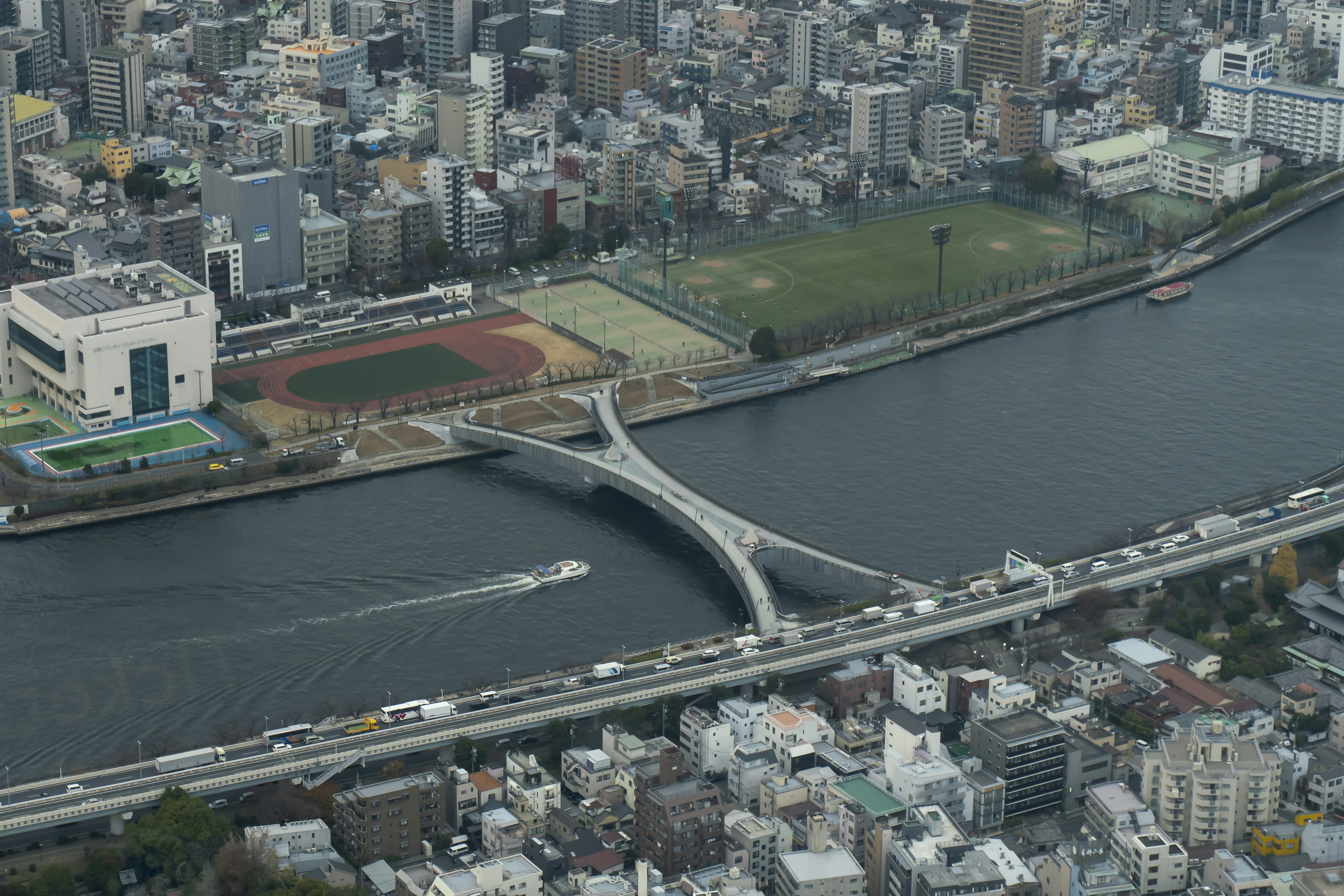 Aerial view of a cityscape featuring a winding river, intersecting roads, and a sports field, showcasing the dynamic interplay of urban life.