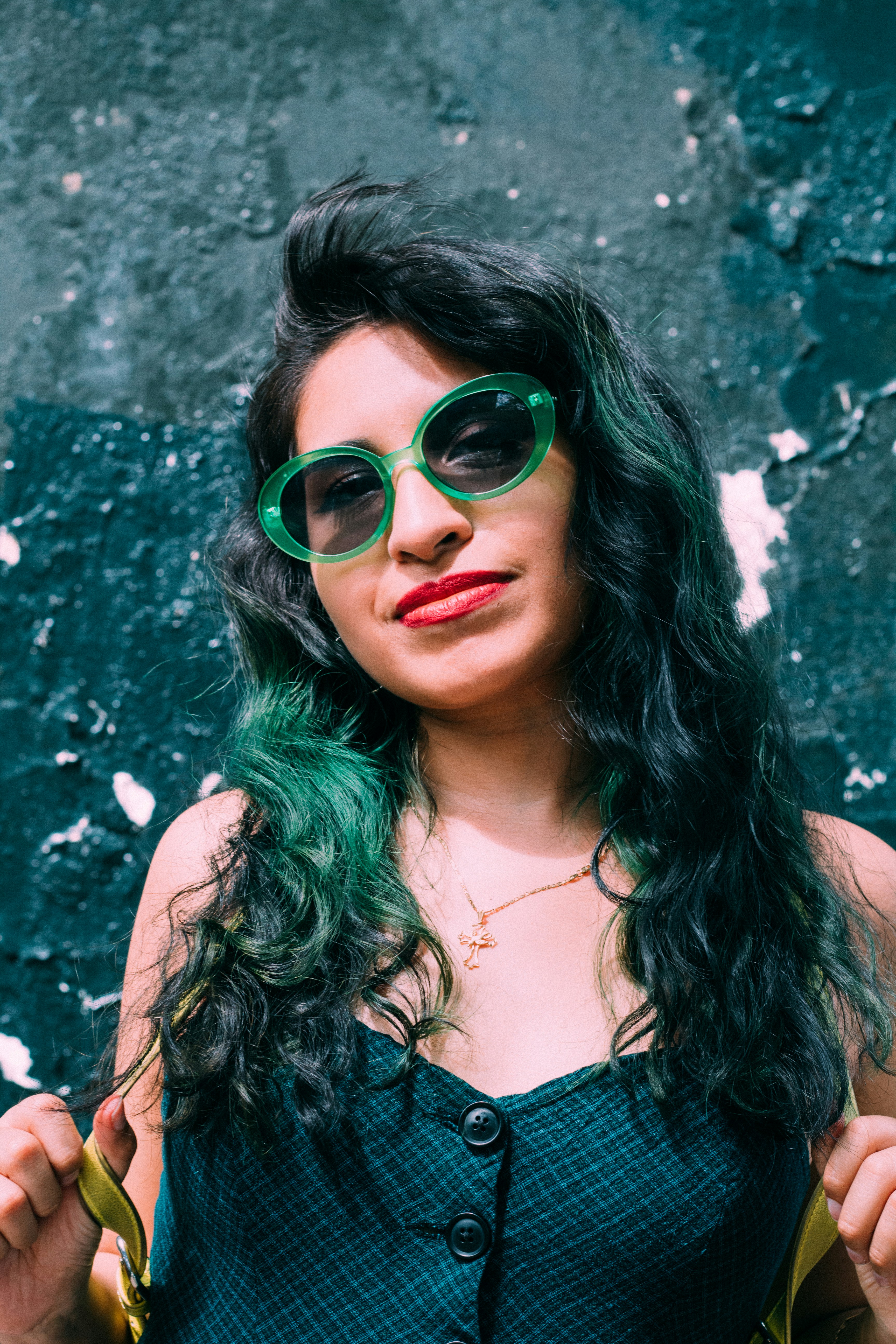 Portrait of a peer at a Bronx playground. She is wearing a green monochrome outfit and she is holding onto the straps of her green backpack. | Young woman with green sunglasses and dyed hair