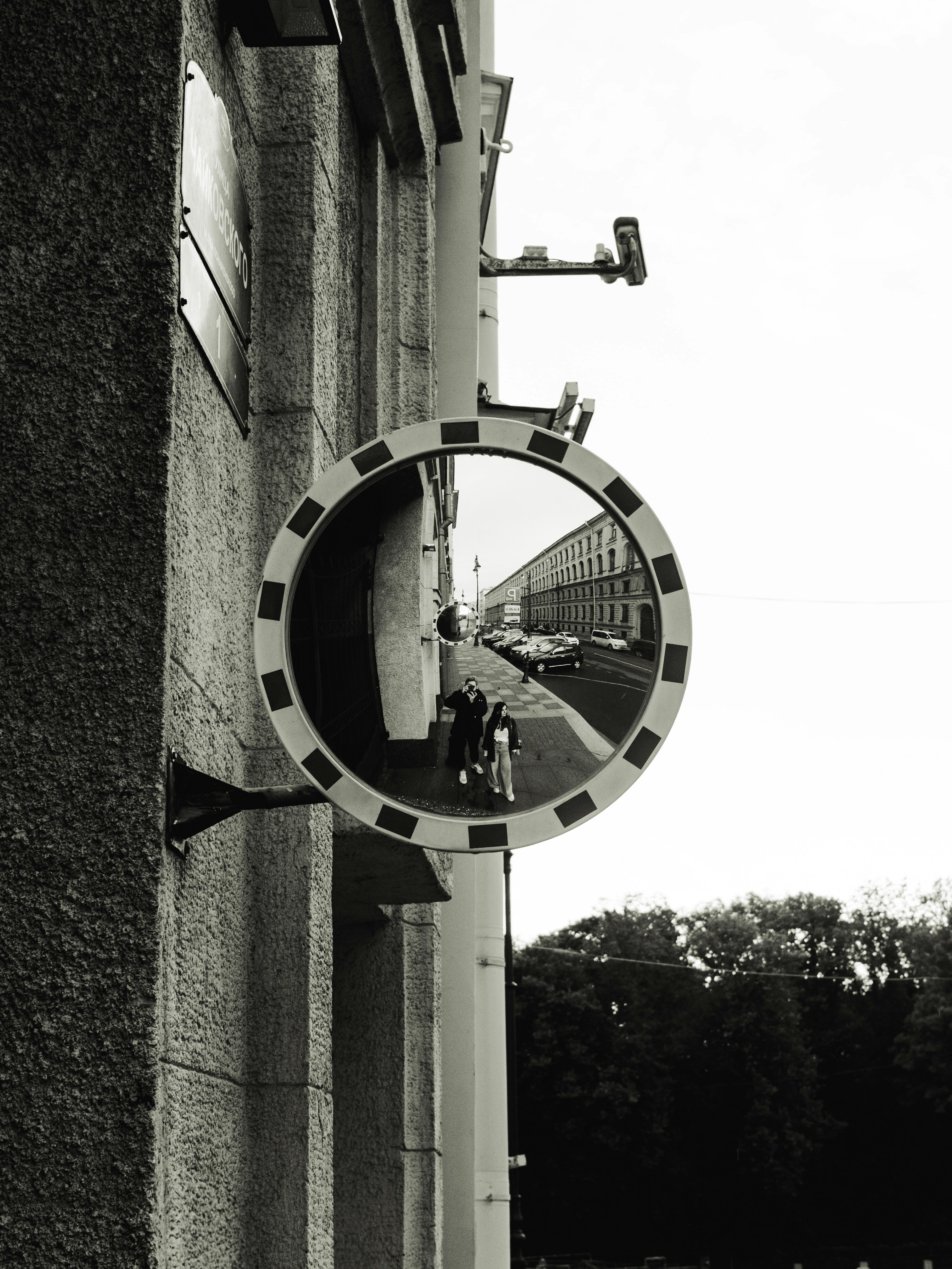 Reflective convex mirror capturing pedestrians and street scene in a city setting.