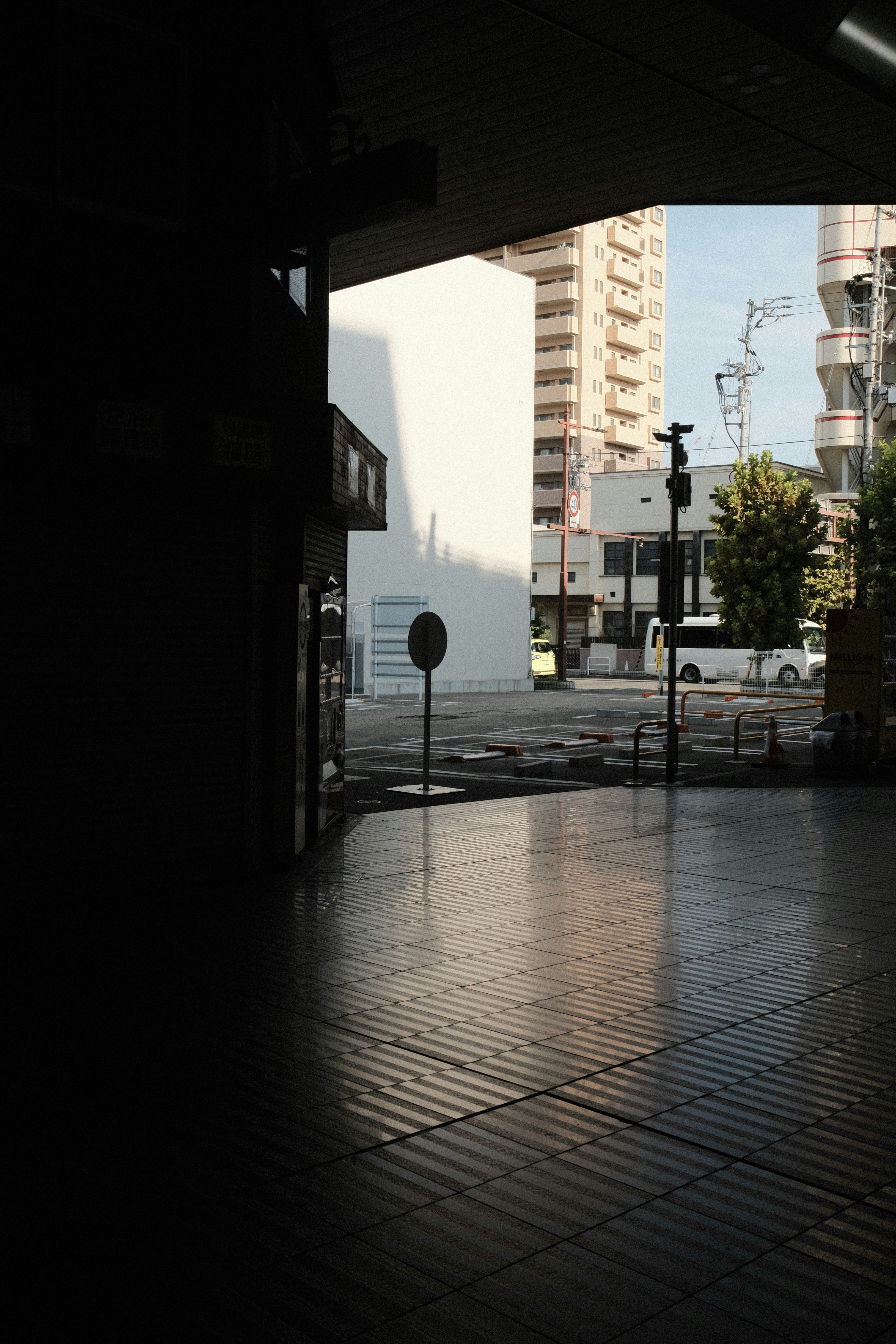 Sunlight casts shadows on a tiled walkway with buildings.