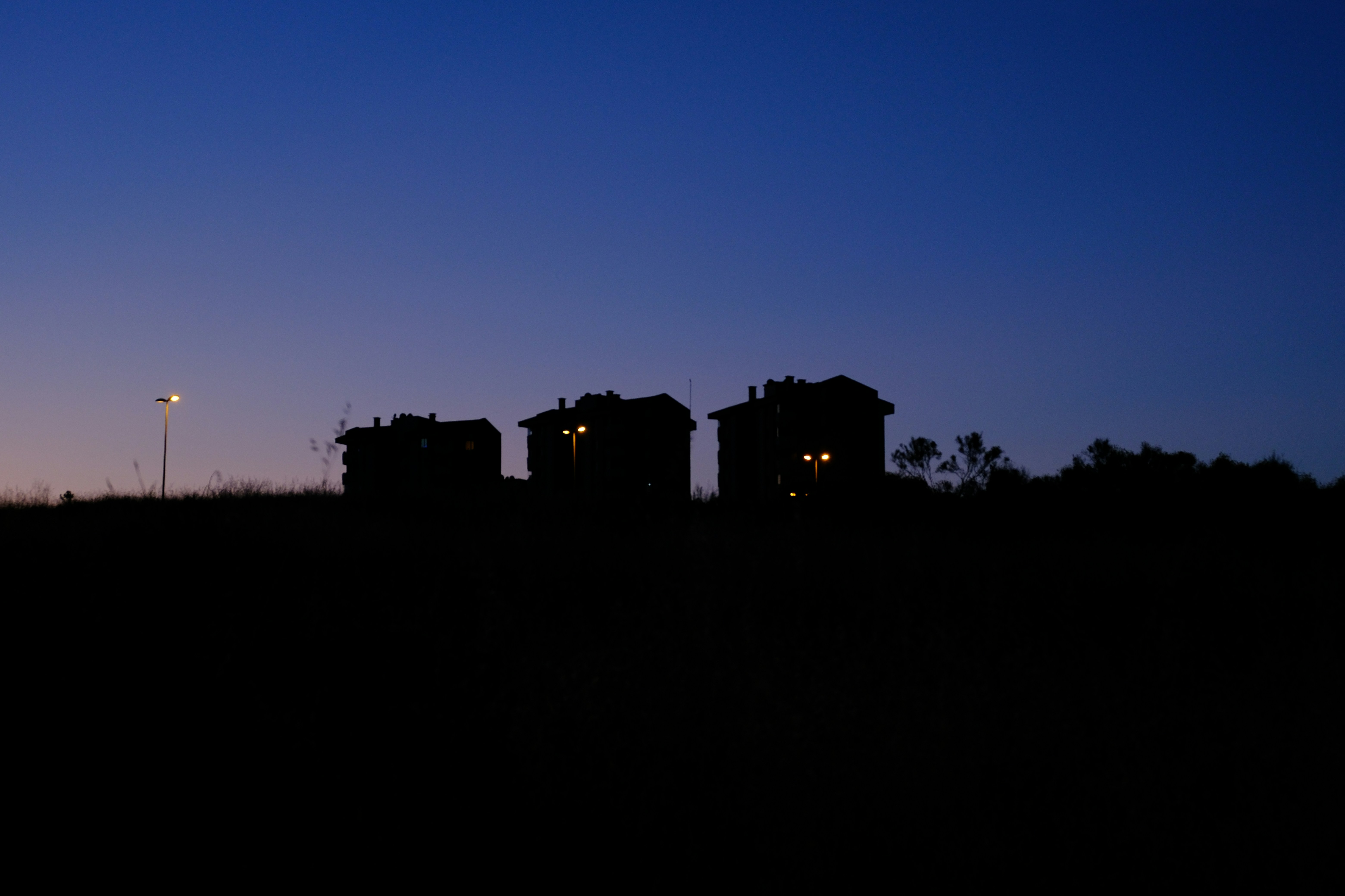 Silhouetted houses on a hill against a twilight sky, with warm lights illuminating their windows.