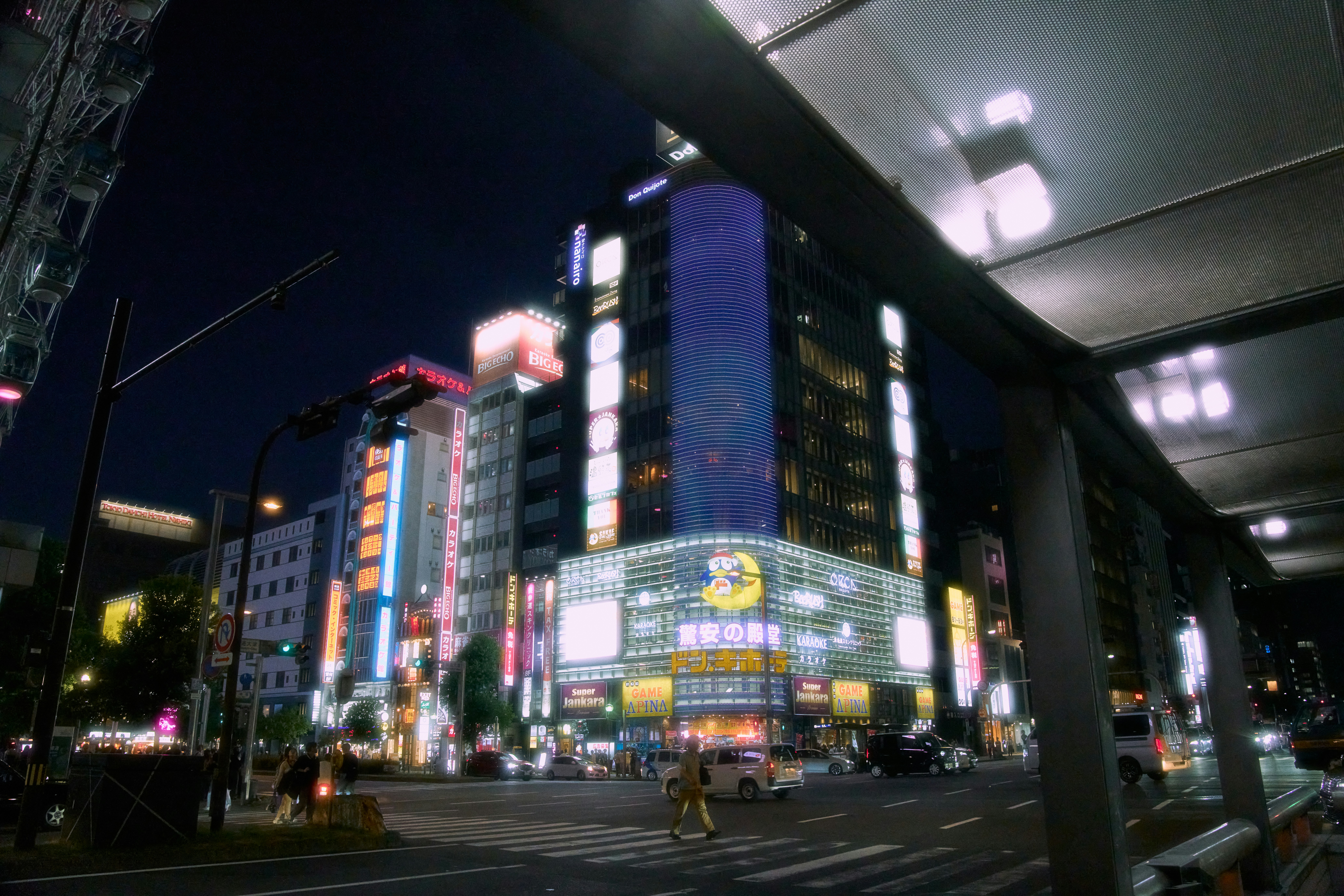 Brightly lit city street at night with tall buildings.