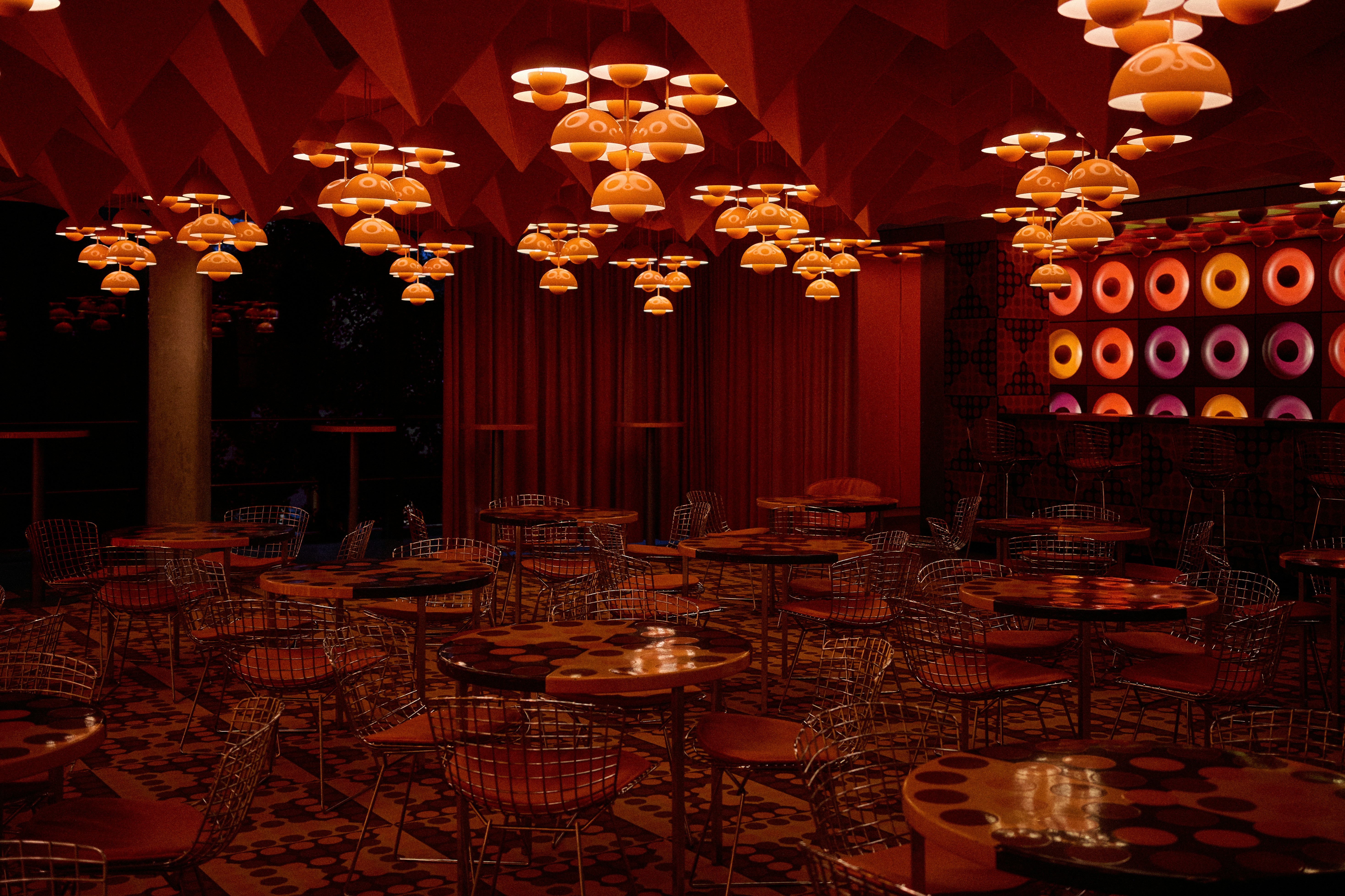 Interior of a modern restaurant featuring vibrant orange lighting and patterned tables, creating a cozy atmosphere.