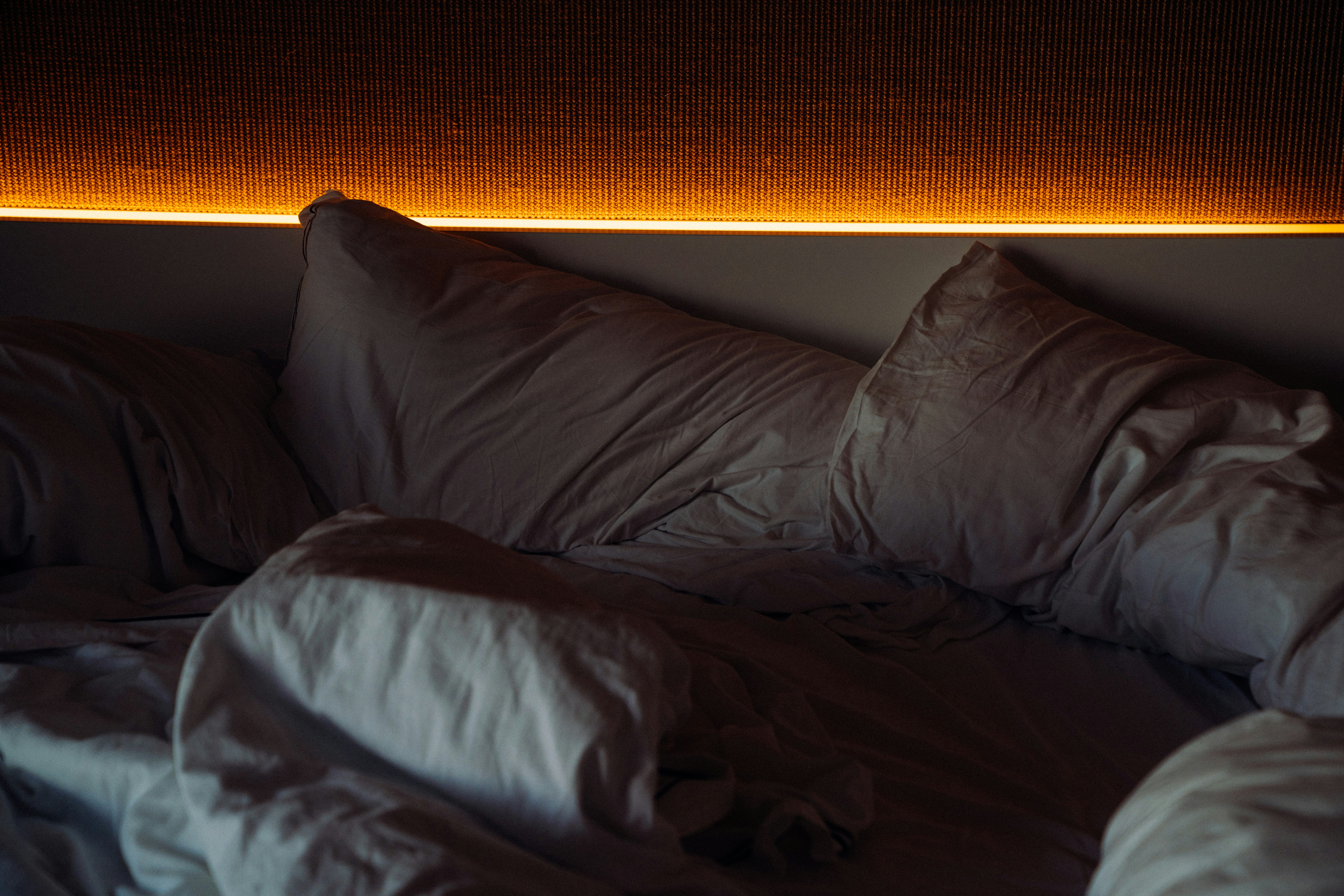Unmade bed with warm ambient lighting above