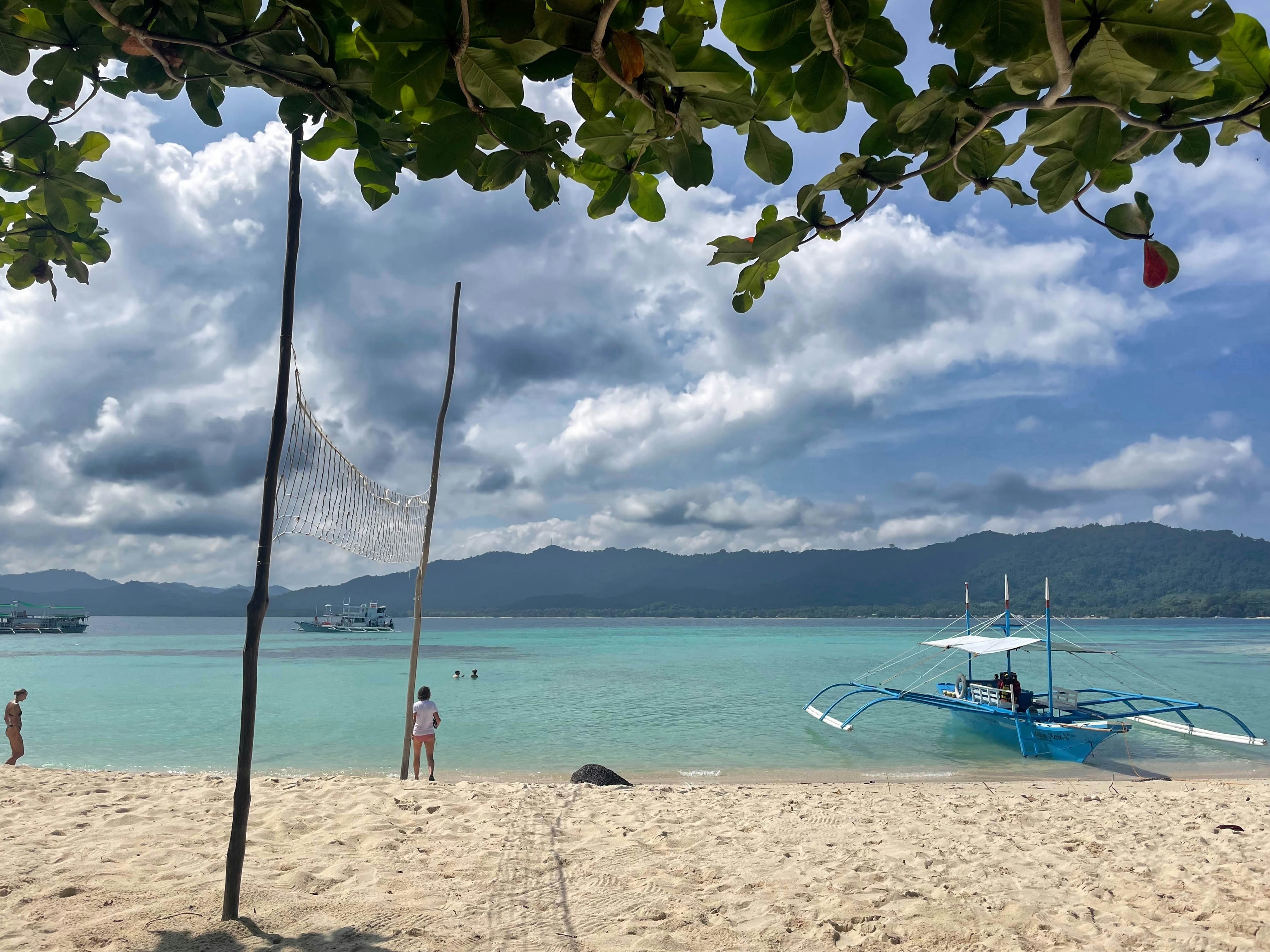 Turquoise Beachfront Calm: Net Stakes, Lone Boat, and Distant Hills