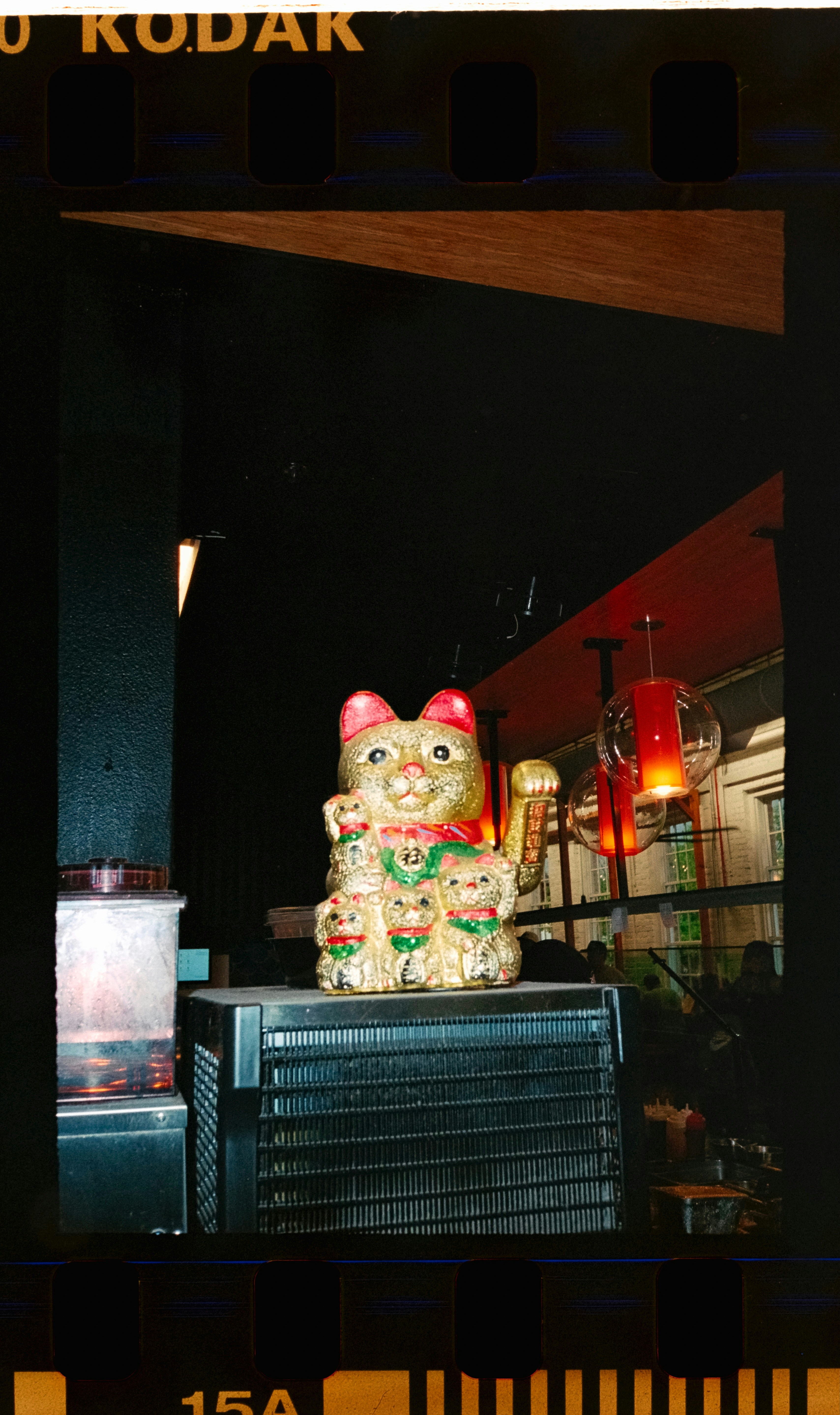 Golden Maneki-neko statue perched atop a shelf in a bustling restaurant, symbolizing good luck and prosperity.