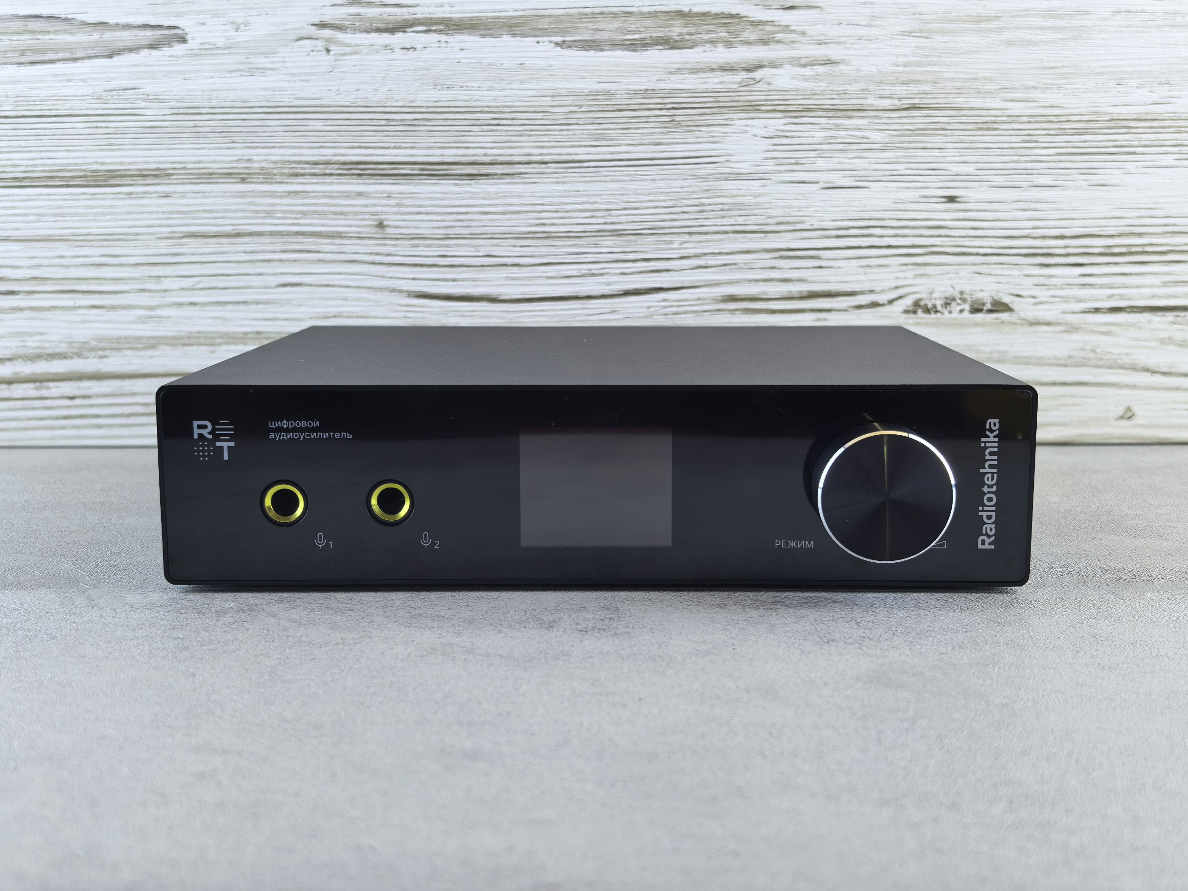 Black audio interface featuring dual headphone jacks and a central display, set against a textured wooden backdrop.