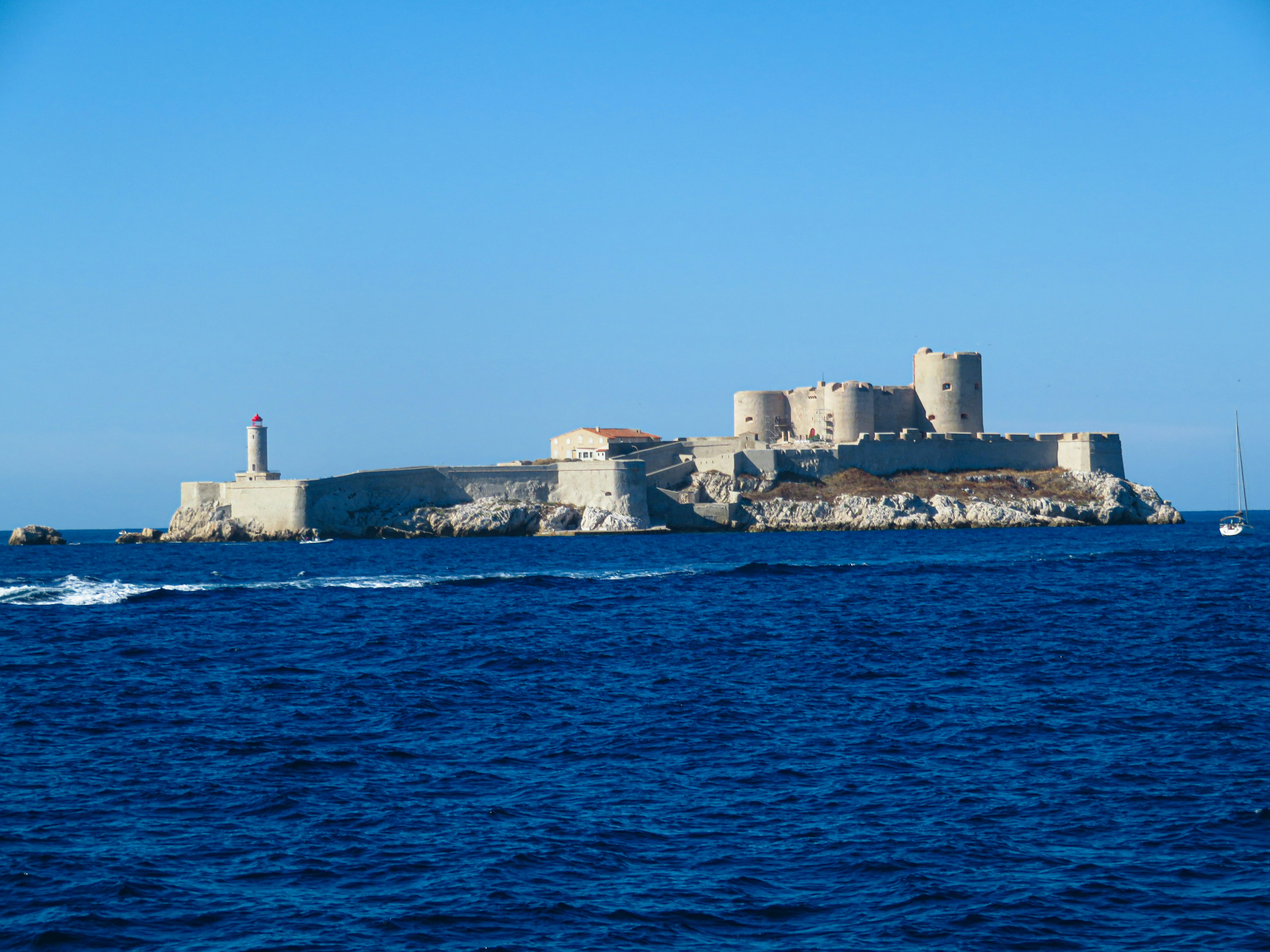 Historic fortress perched on a rocky island, with a lighthouse standing guard against the azure sea backdrop.
