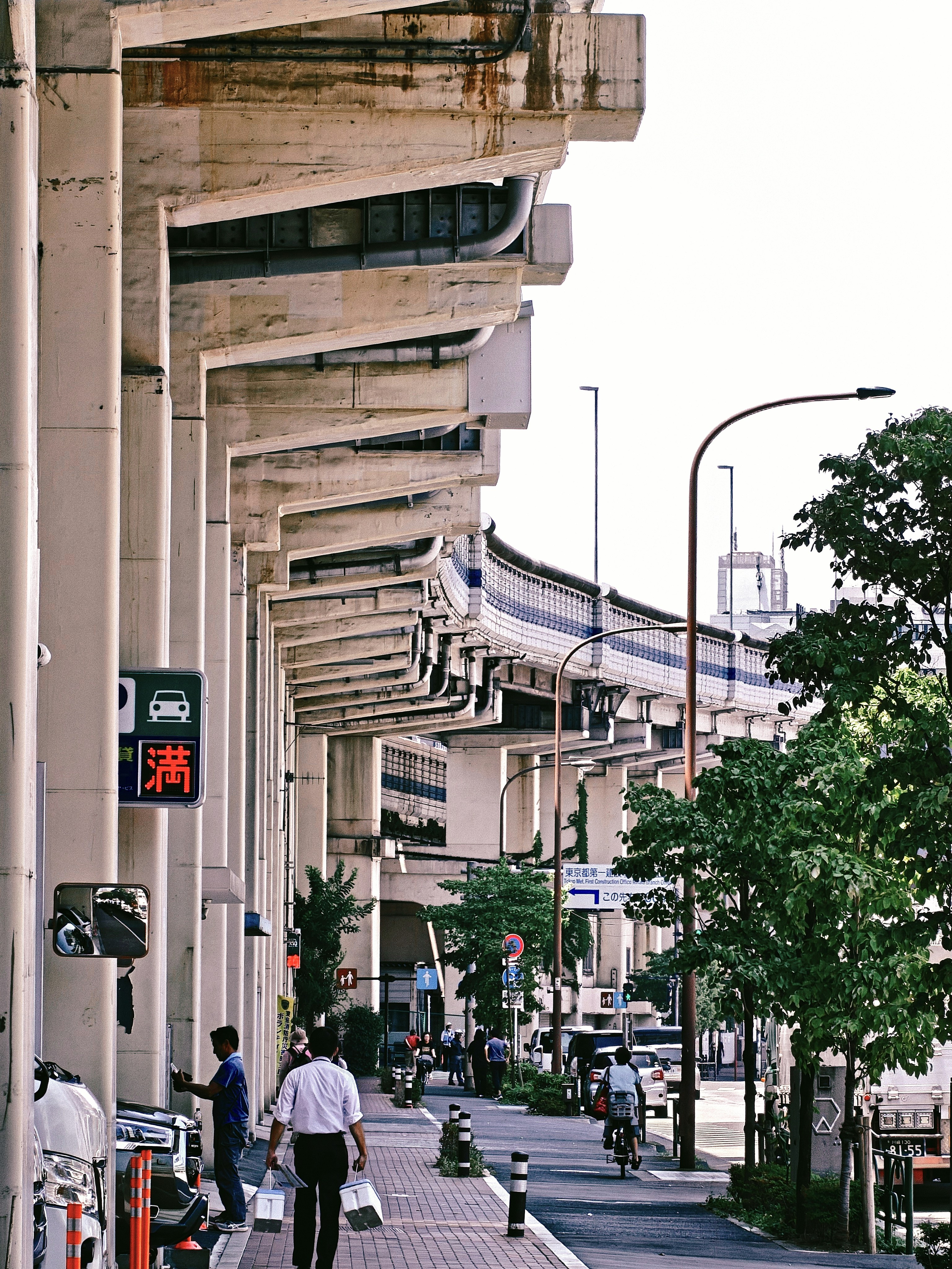 People walk along a city street under an elevated highway.