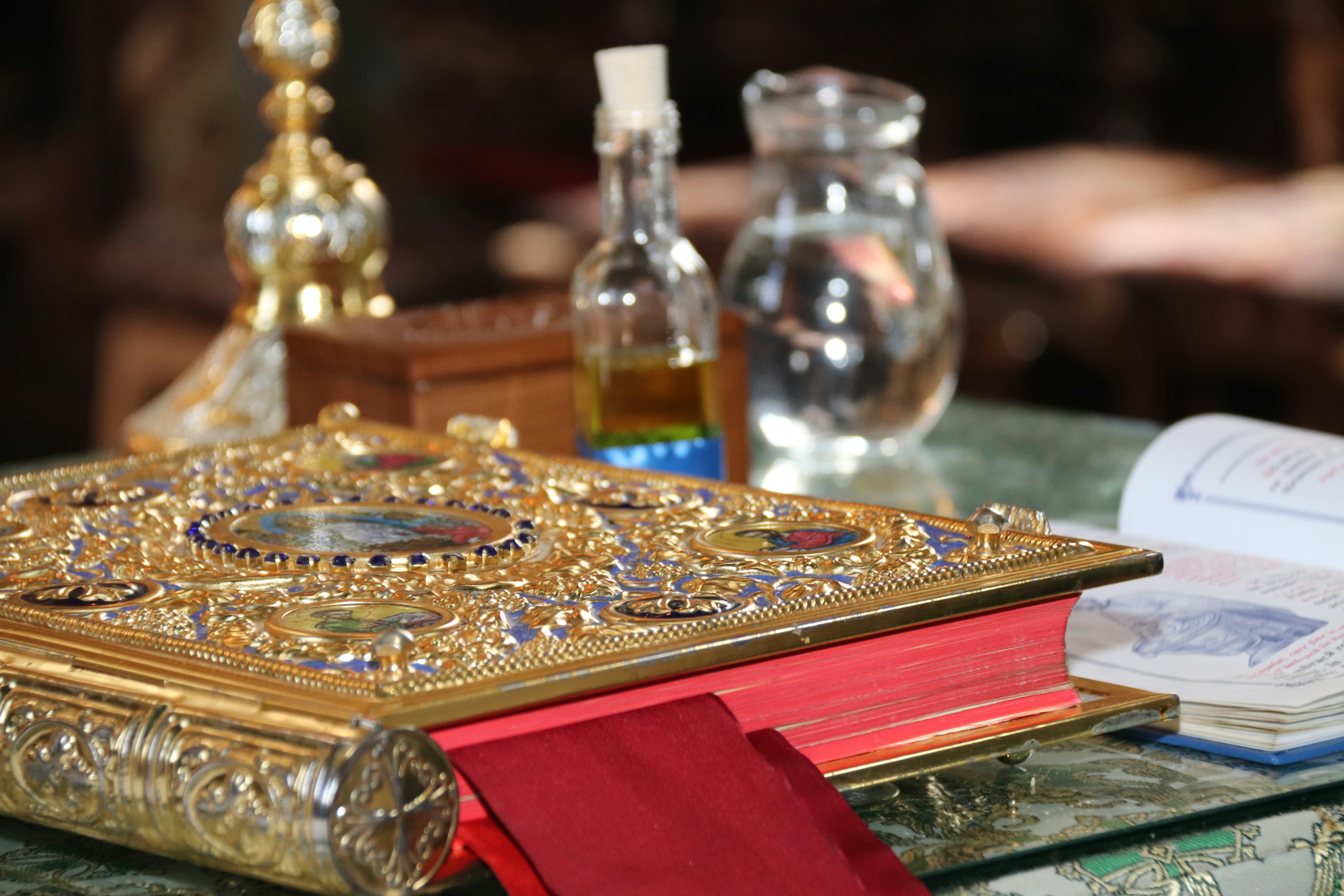 Intricately designed golden book resting on a table, accompanied by a glass of water and a small bottle, showcasing the beauty of religious artifacts.