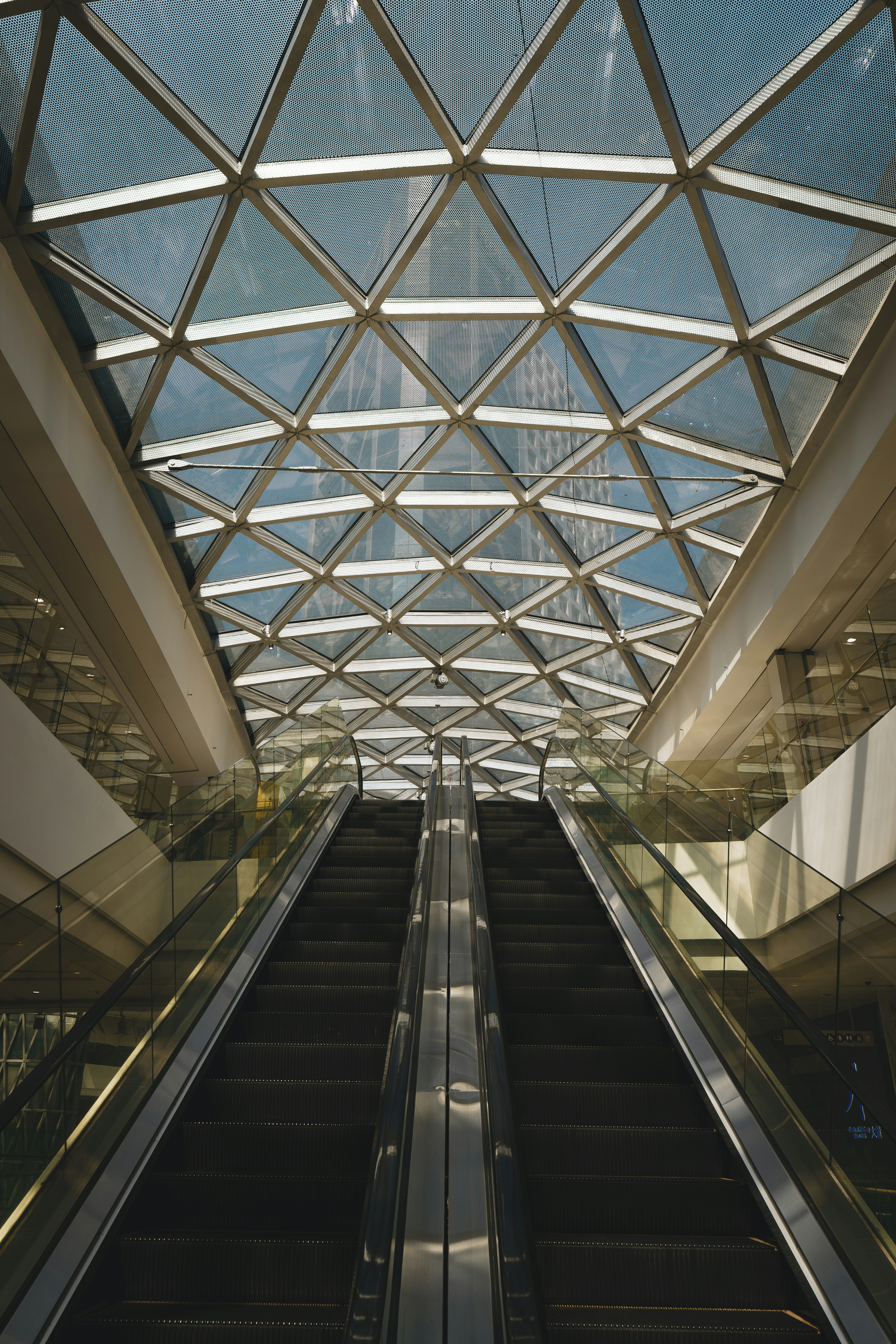 Modern escalators leading up to a geometric glass ceiling.