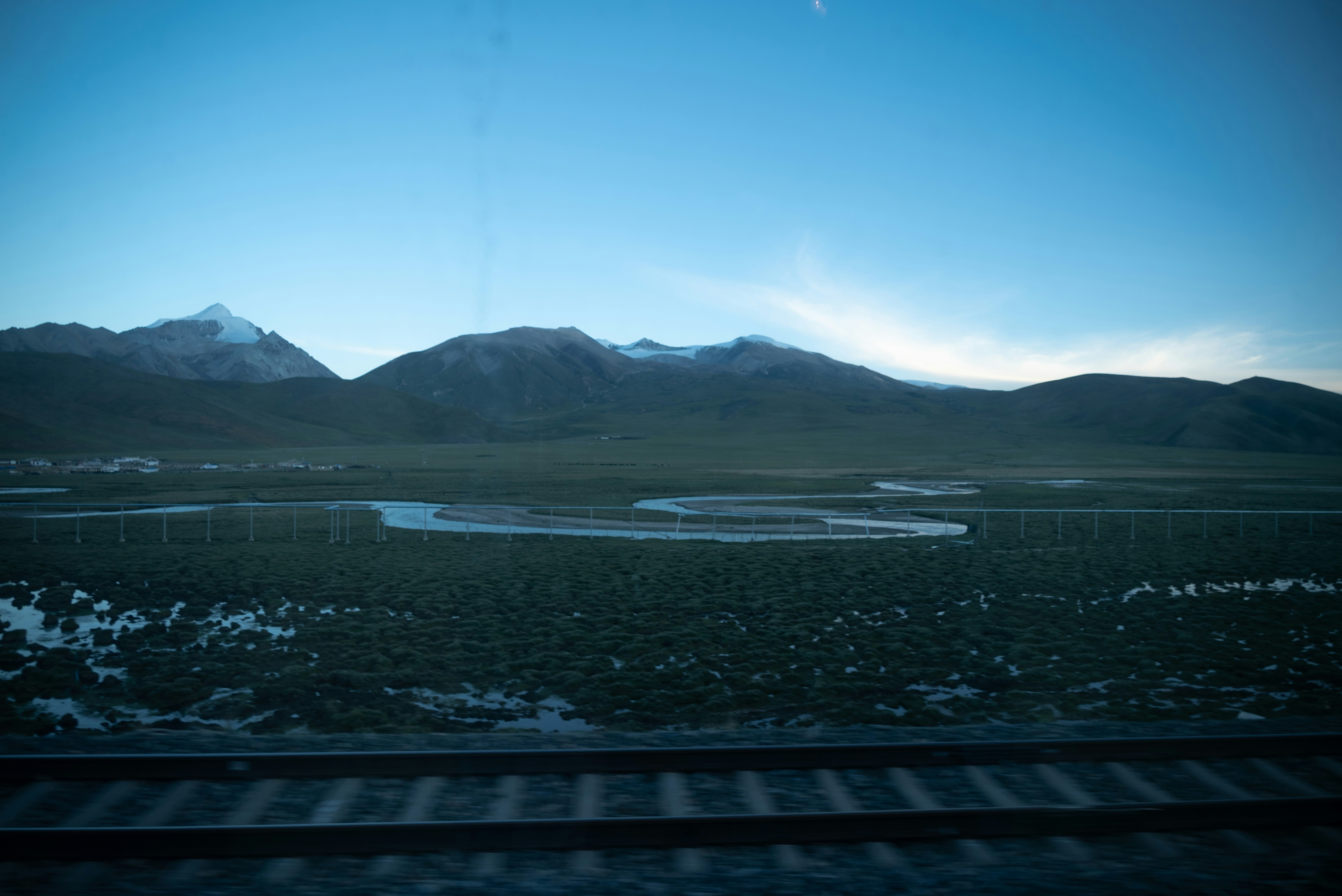 Rings on the Plain: A Blue-Tinted Wake beneath Snowy Peaks