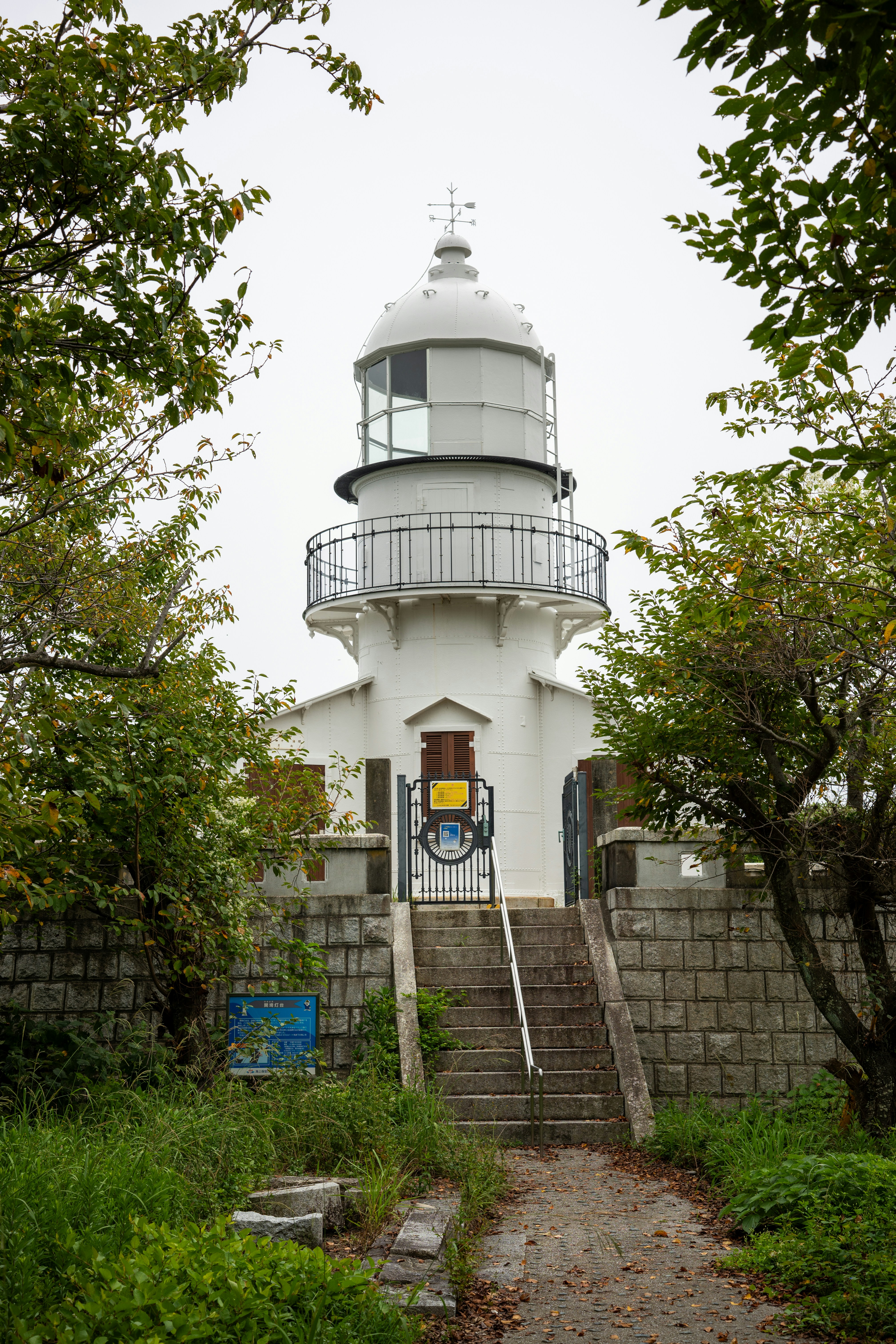 Beacon at the Gate: White Lighthouse Framed by Green Foliage