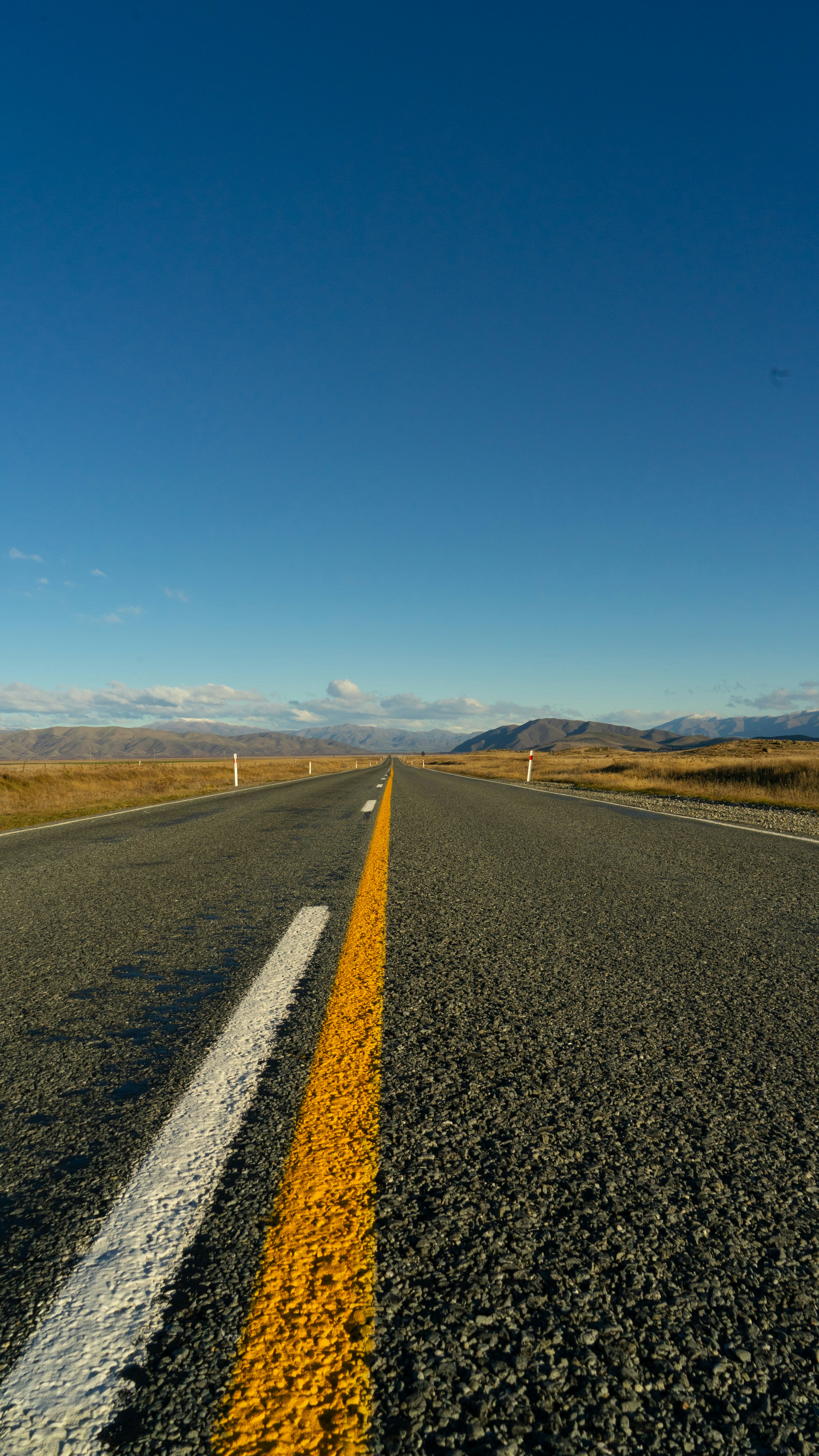 An empty highway stretches towards distant mountains under a clear sky.