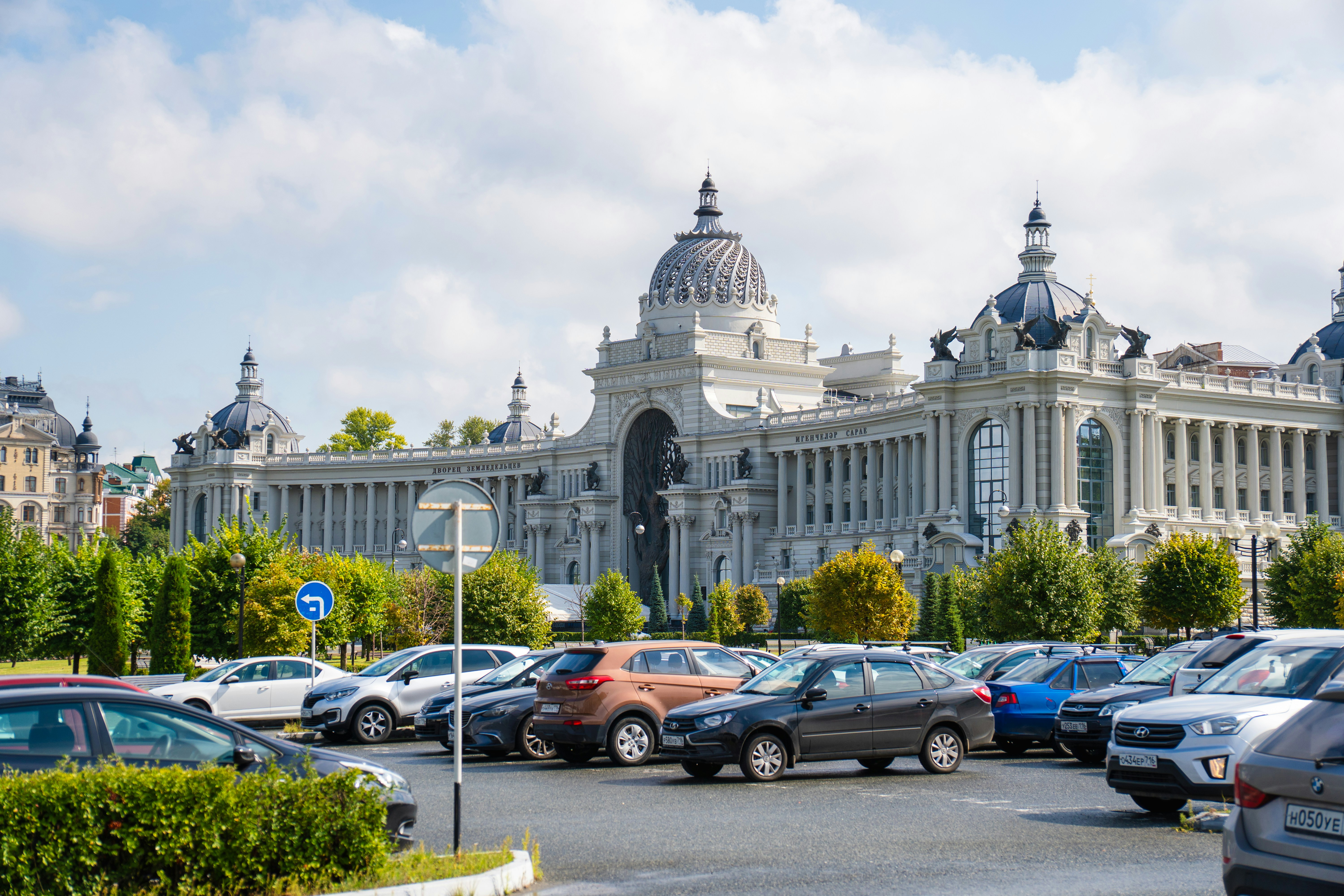 Imposing historical building with ornate architecture, surrounded by a bustling parking lot filled with various vehicles.