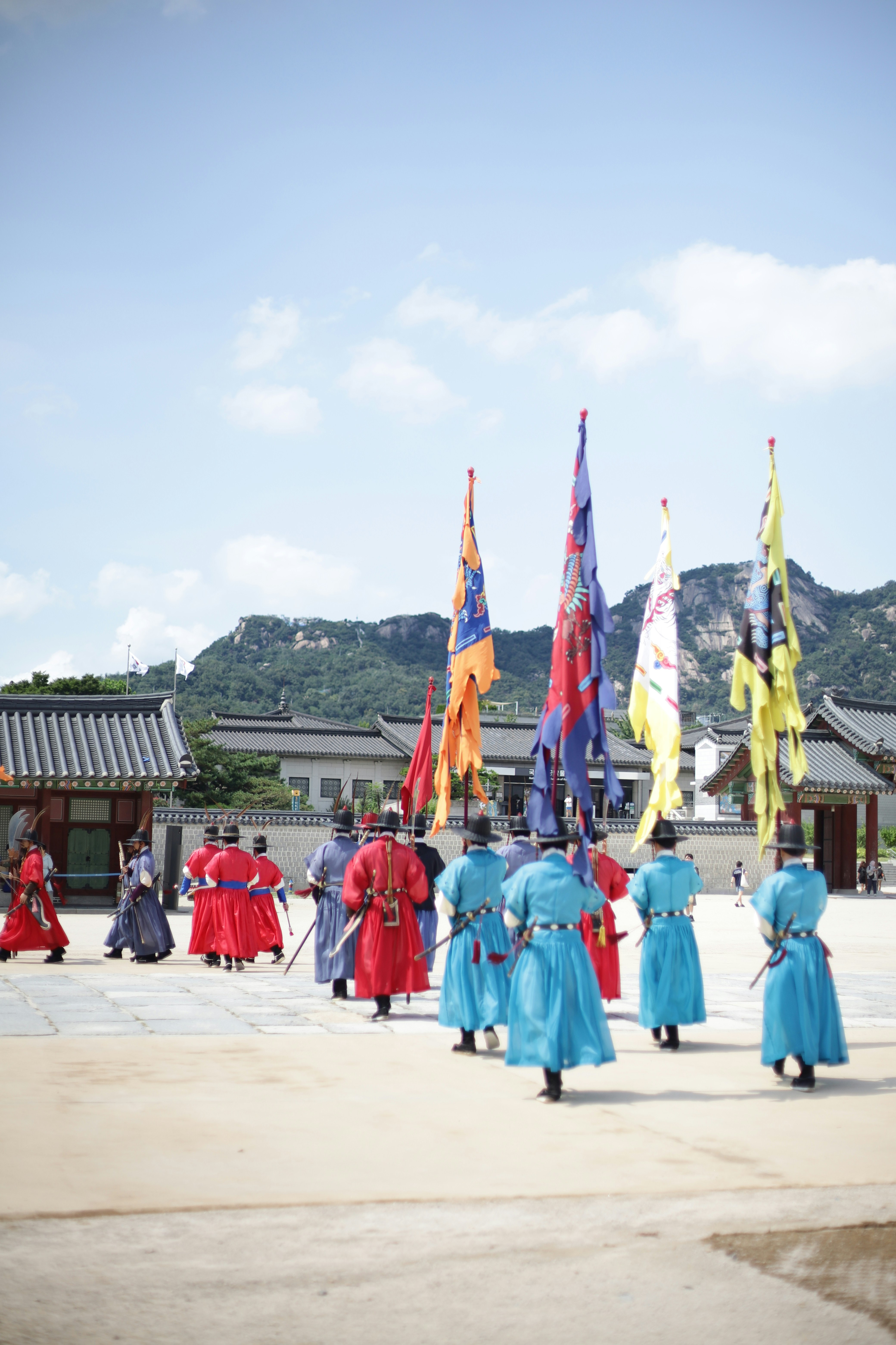 Guards in traditional korean attire march with colorful flags.
