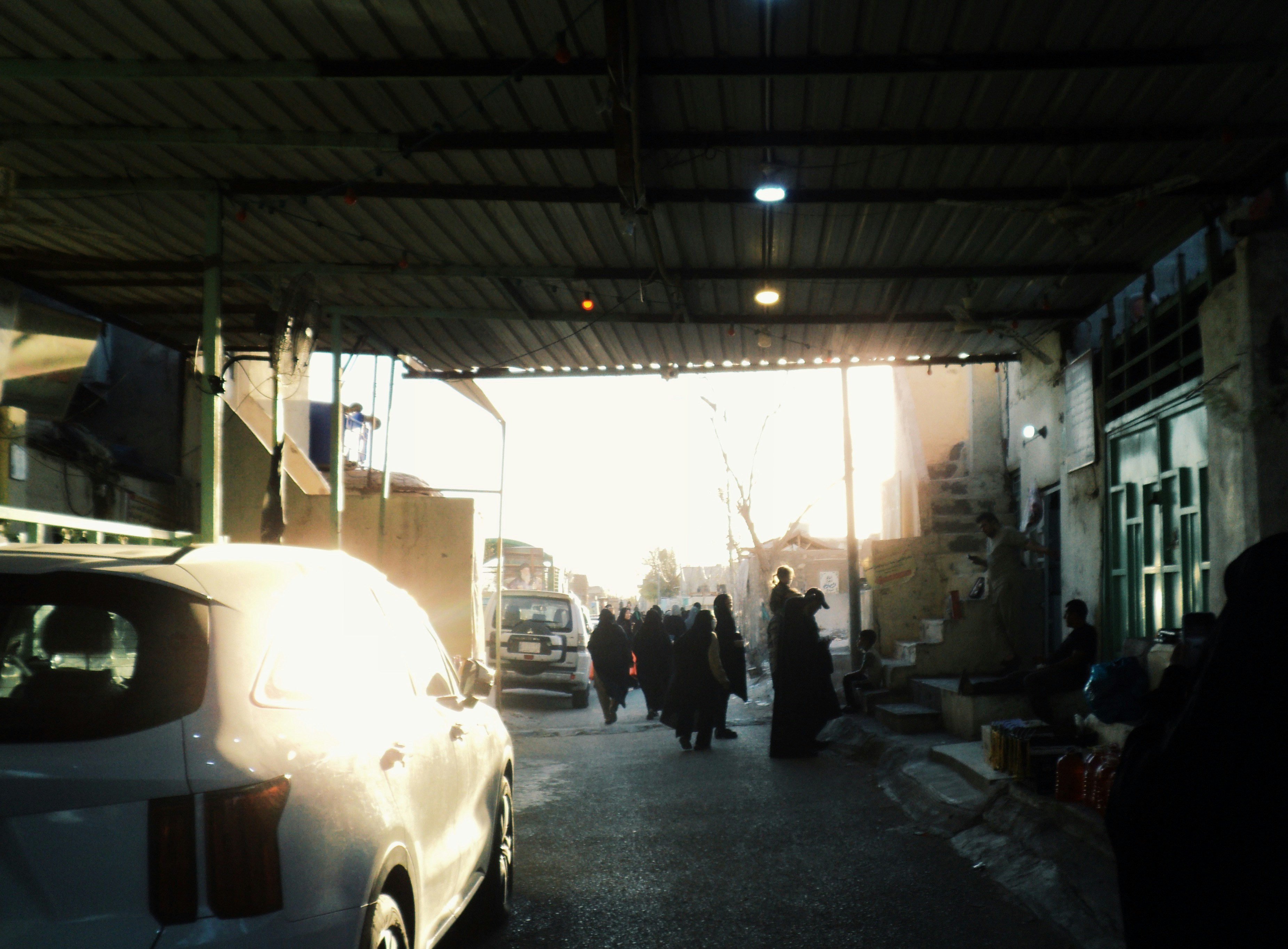 A portrait of a moment, captured in light and shadow. | People walking down a sunlit street with cars.